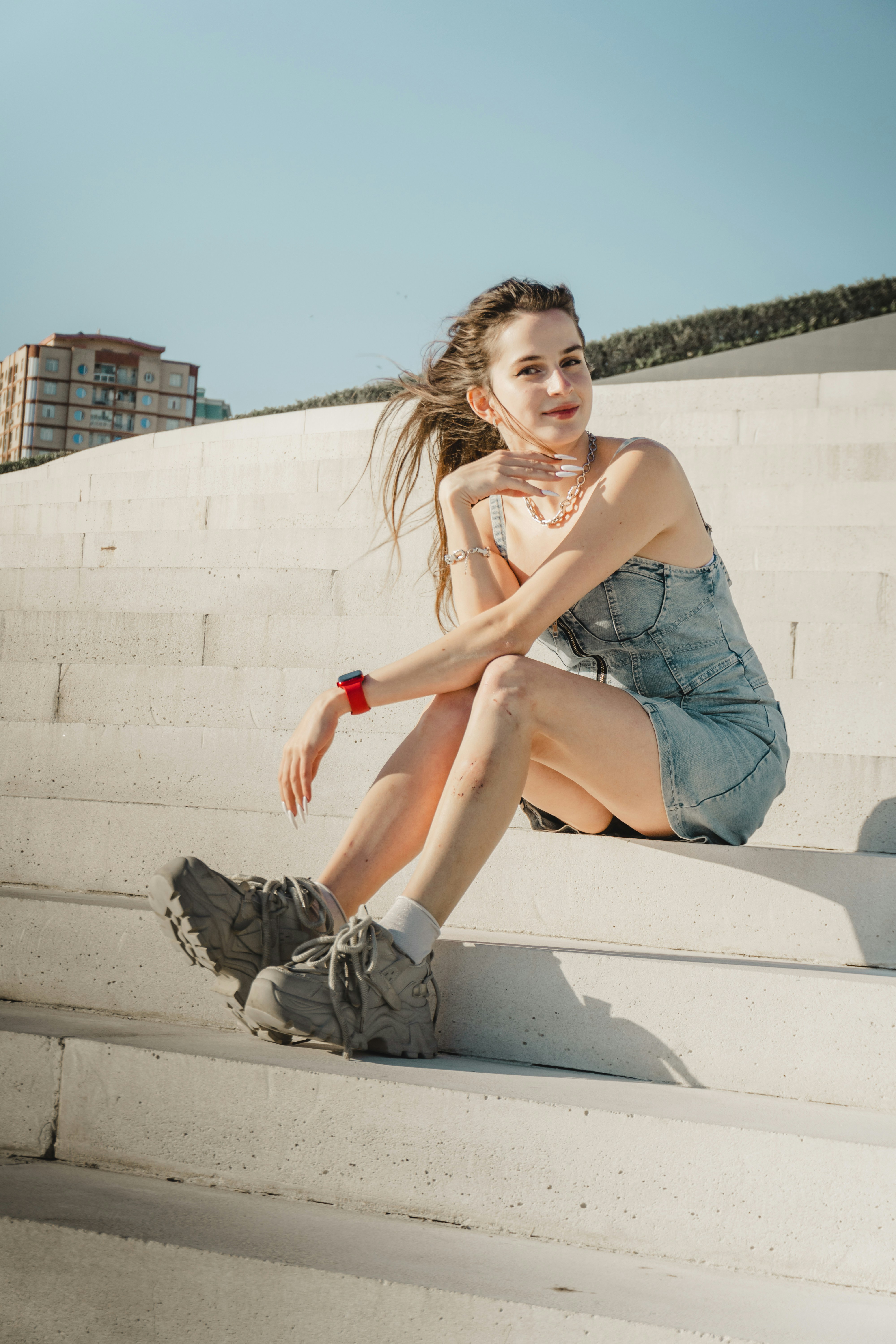 Young woman in denim dress sitting on concrete steps