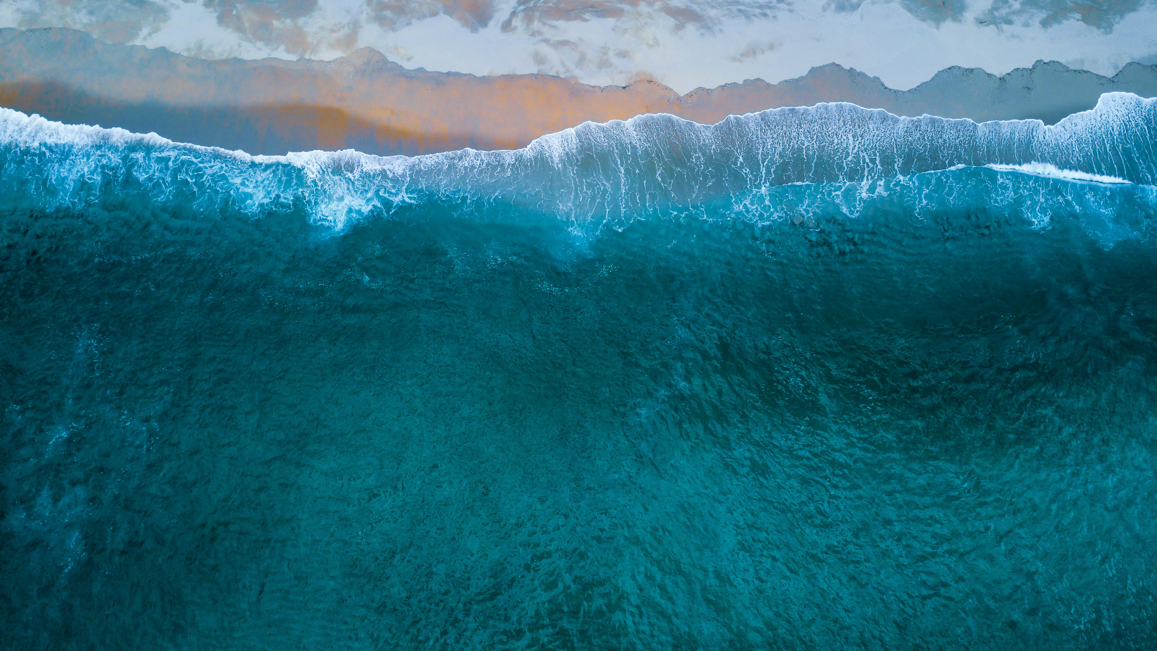 Ocean waves crashing on a sandy beach from above