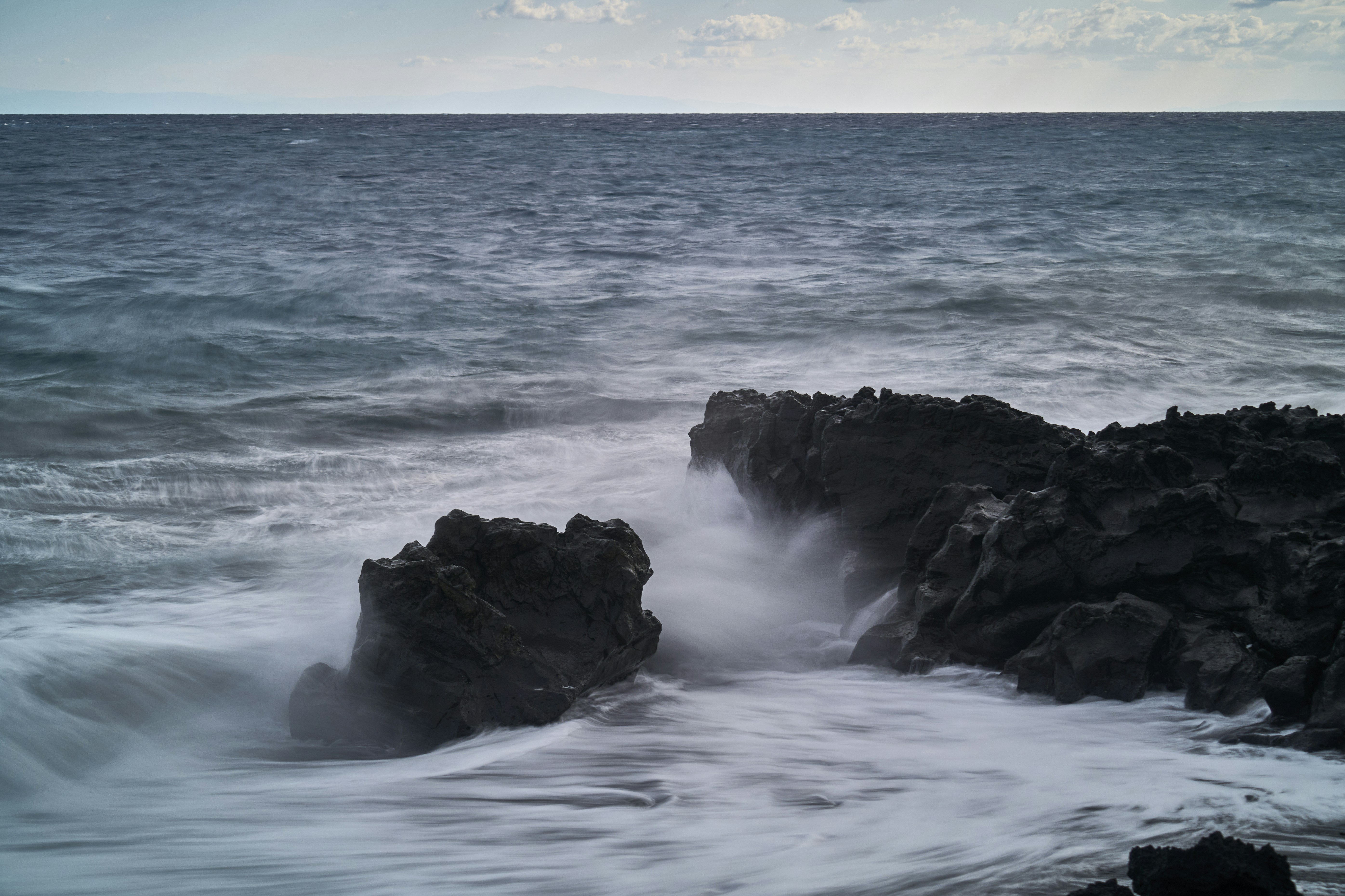 Waves crash against dark volcanic rocks on the coast.