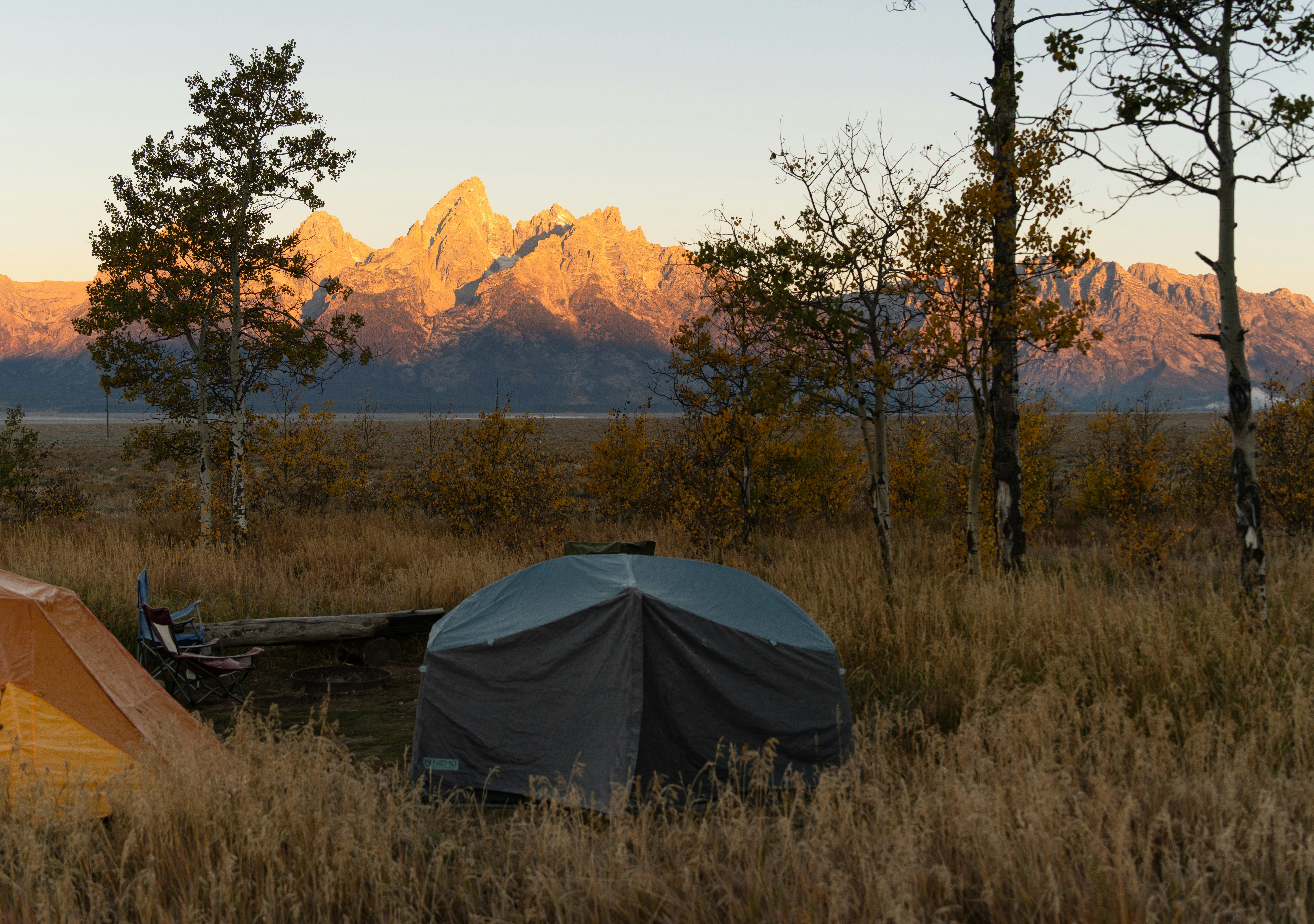Golden Hour at the Camp: Tents Nestled Before a Crimson Mountain Ridge