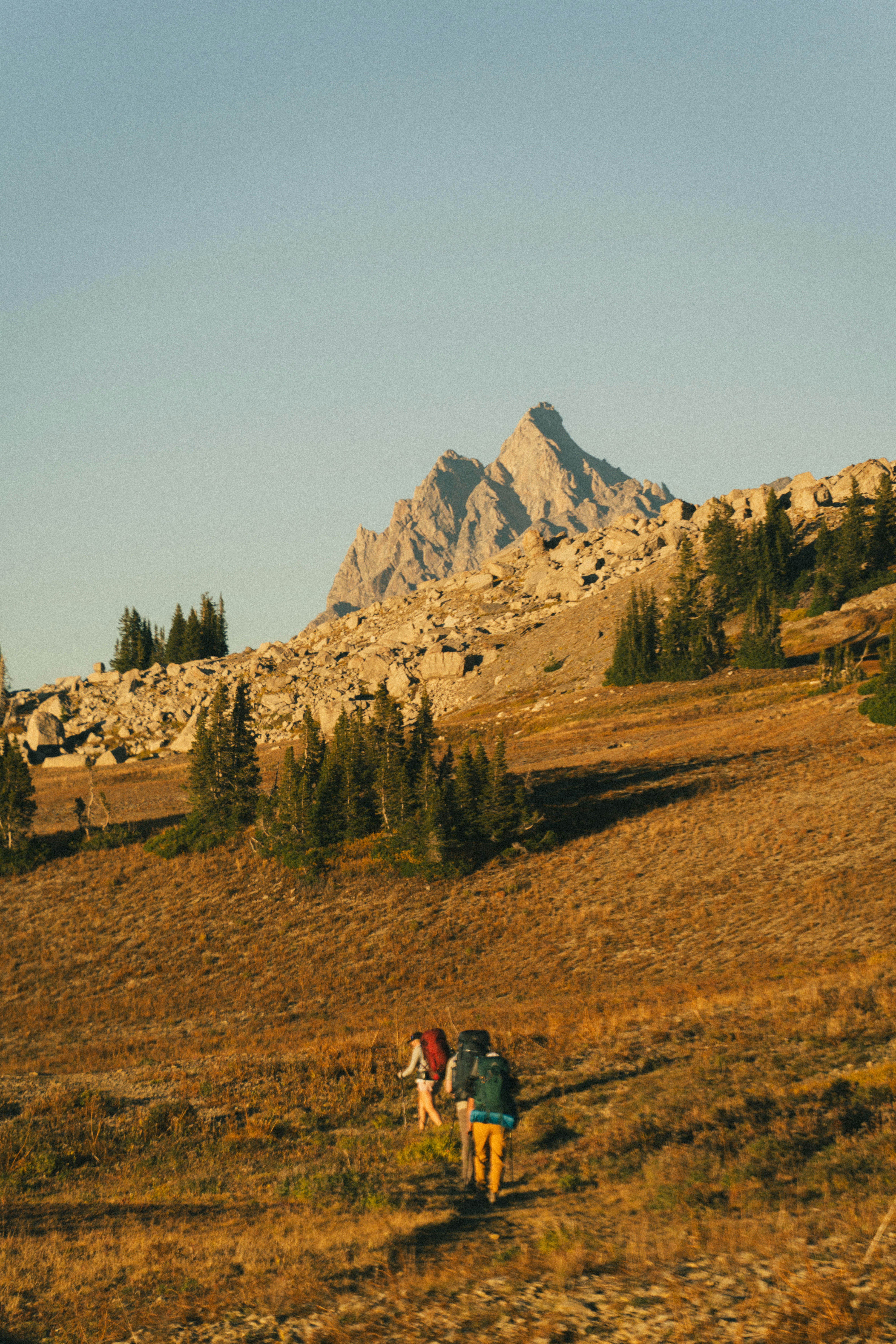 Hikers Converge on a Sunlit Ascent Beneath a Jagged Alpine Peak