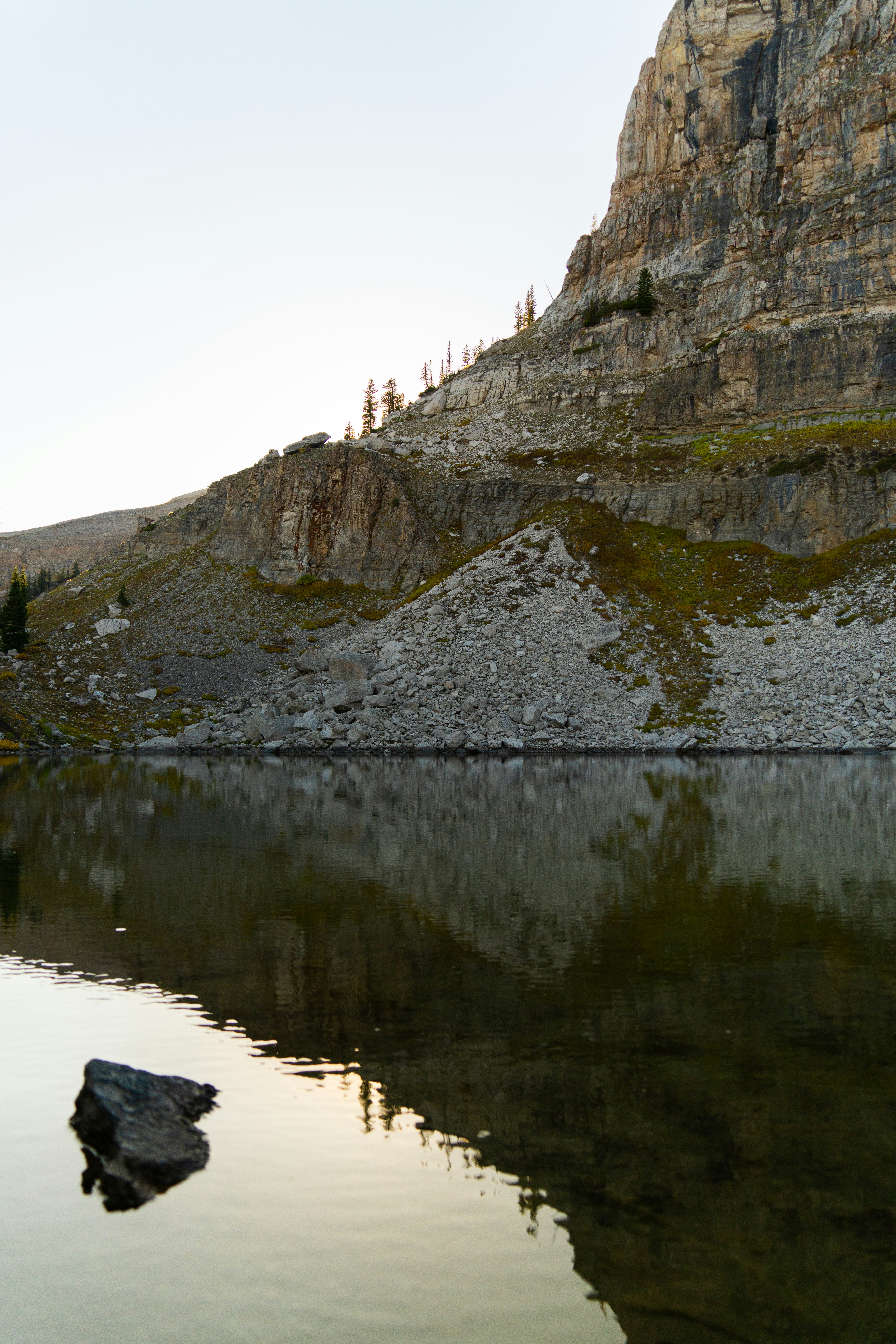 A serene mountain landscape reflecting on a still lake, showcasing rugged cliffs and a tranquil atmosphere.