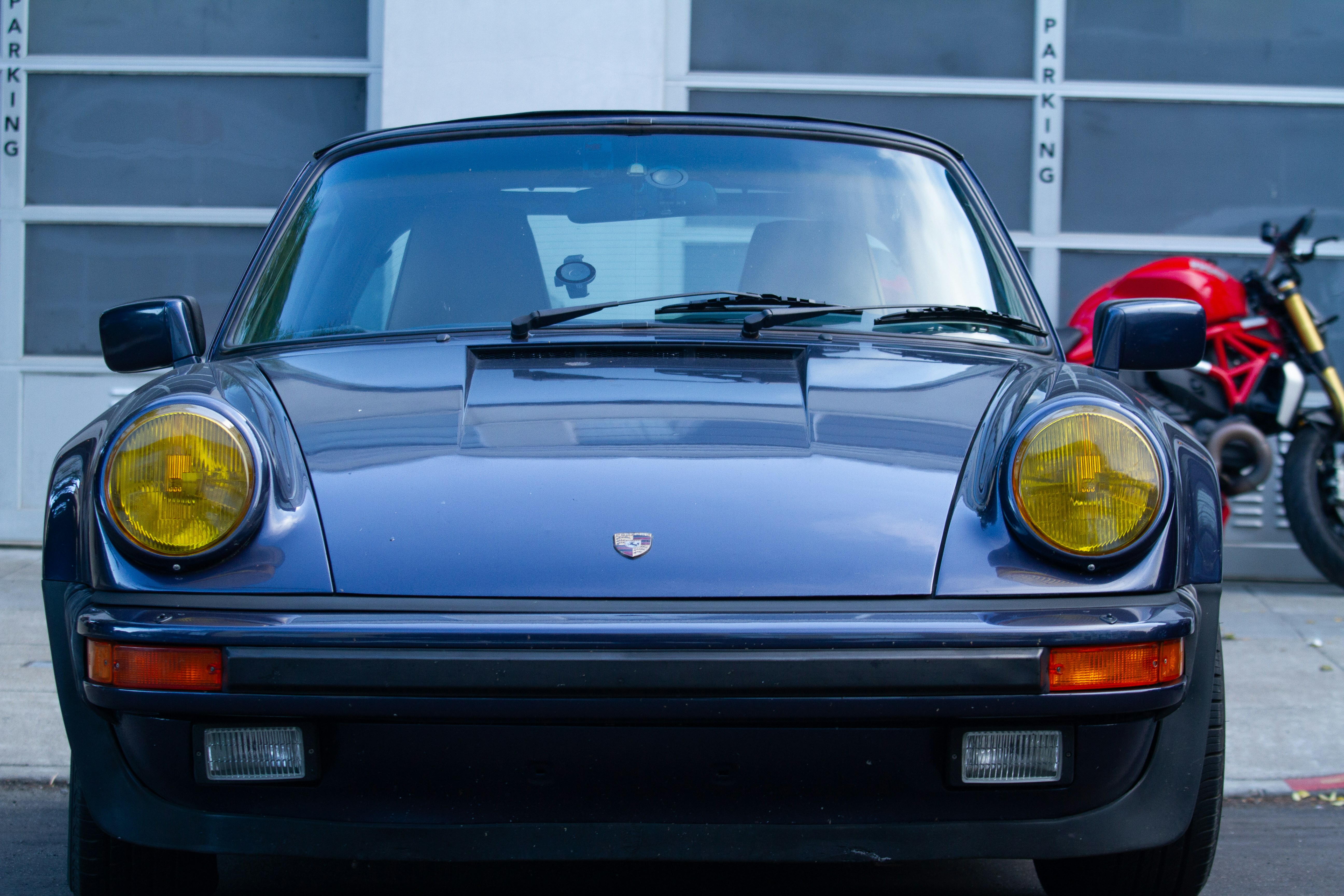 Front view of a vintage Porsche with distinctive yellow headlights, parked in an urban setting.