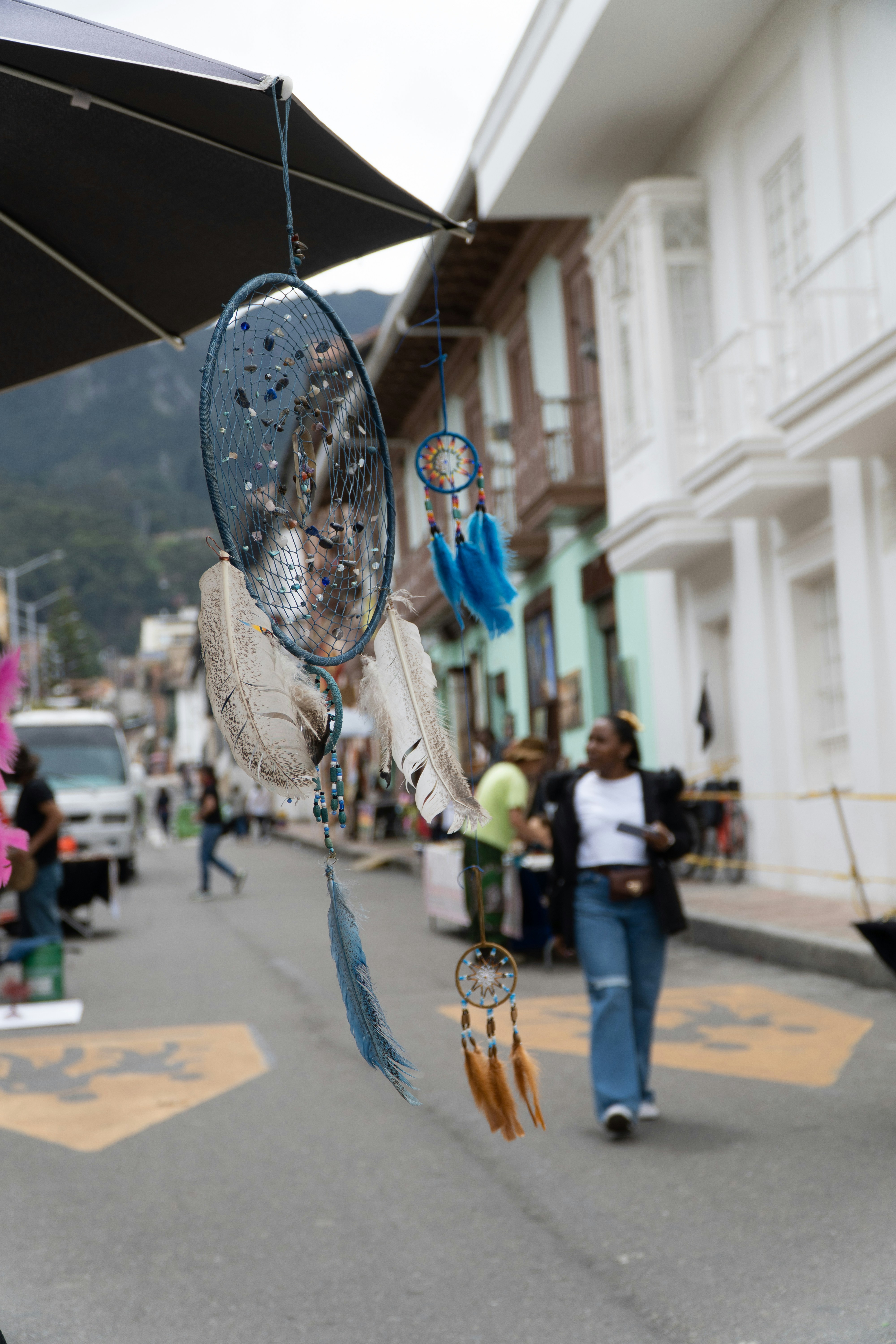 Colorful dreamcatcher adorned with feathers sways gently in the breeze, framed by a bustling street scene. The vibrant backdrop showcases local culture and craftsmanship.