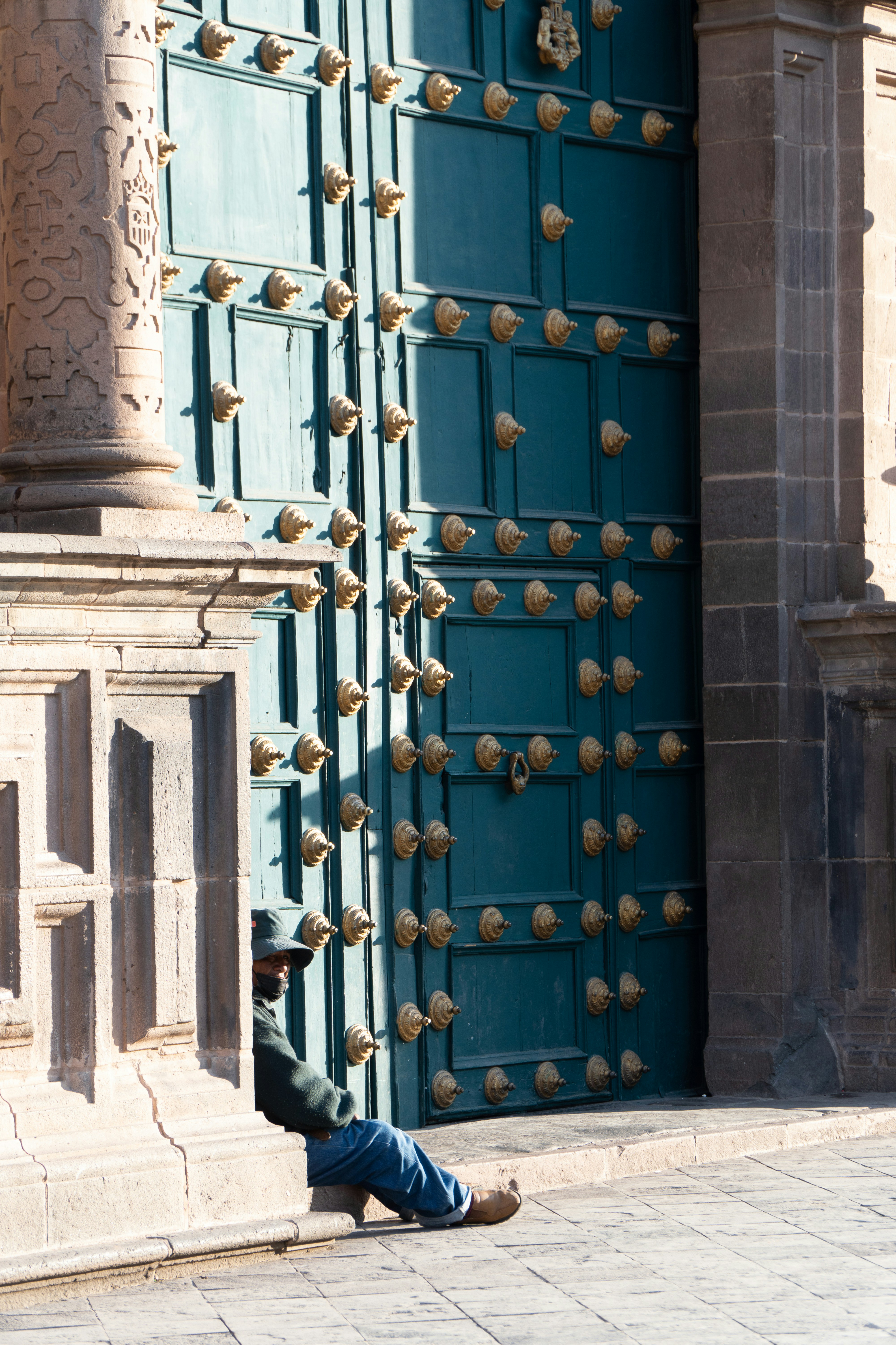 Man resting by large ornate teal door