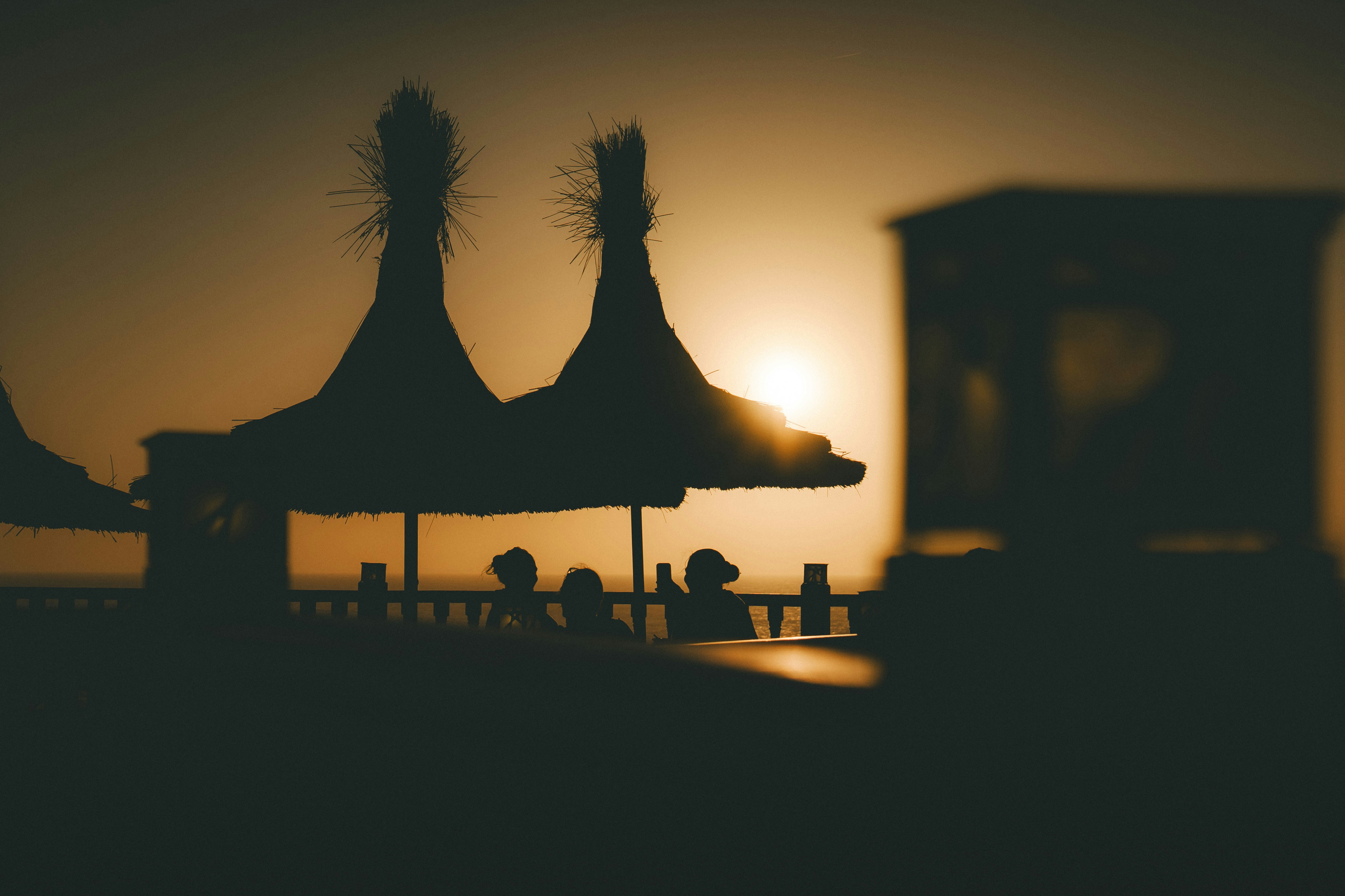 Horizon of Light: Silhouettes Beneath a Sunset Palapa Row