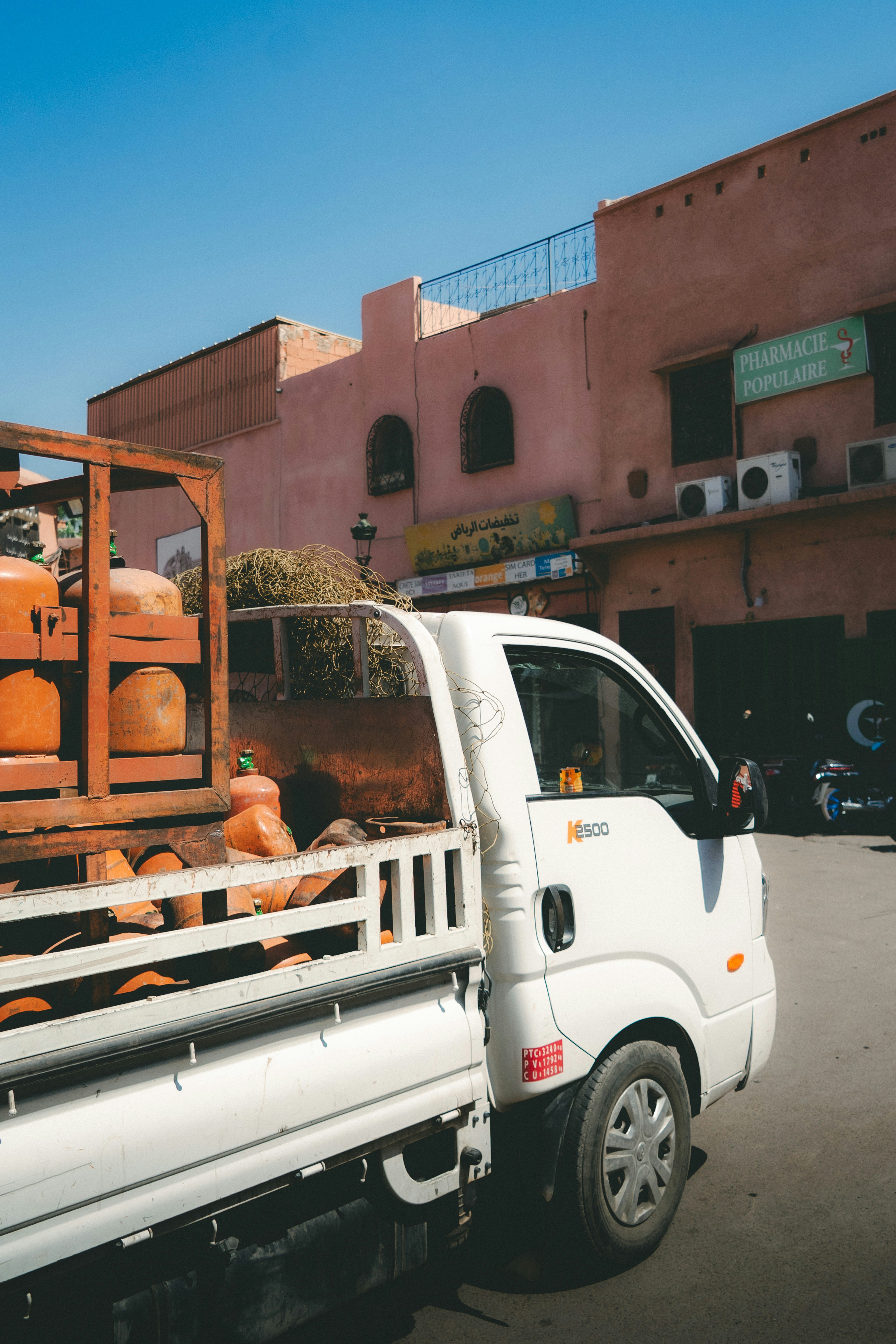 A small truck loaded with clay pots navigates the bustling streets of Marrakech, framed by vibrant local architecture.