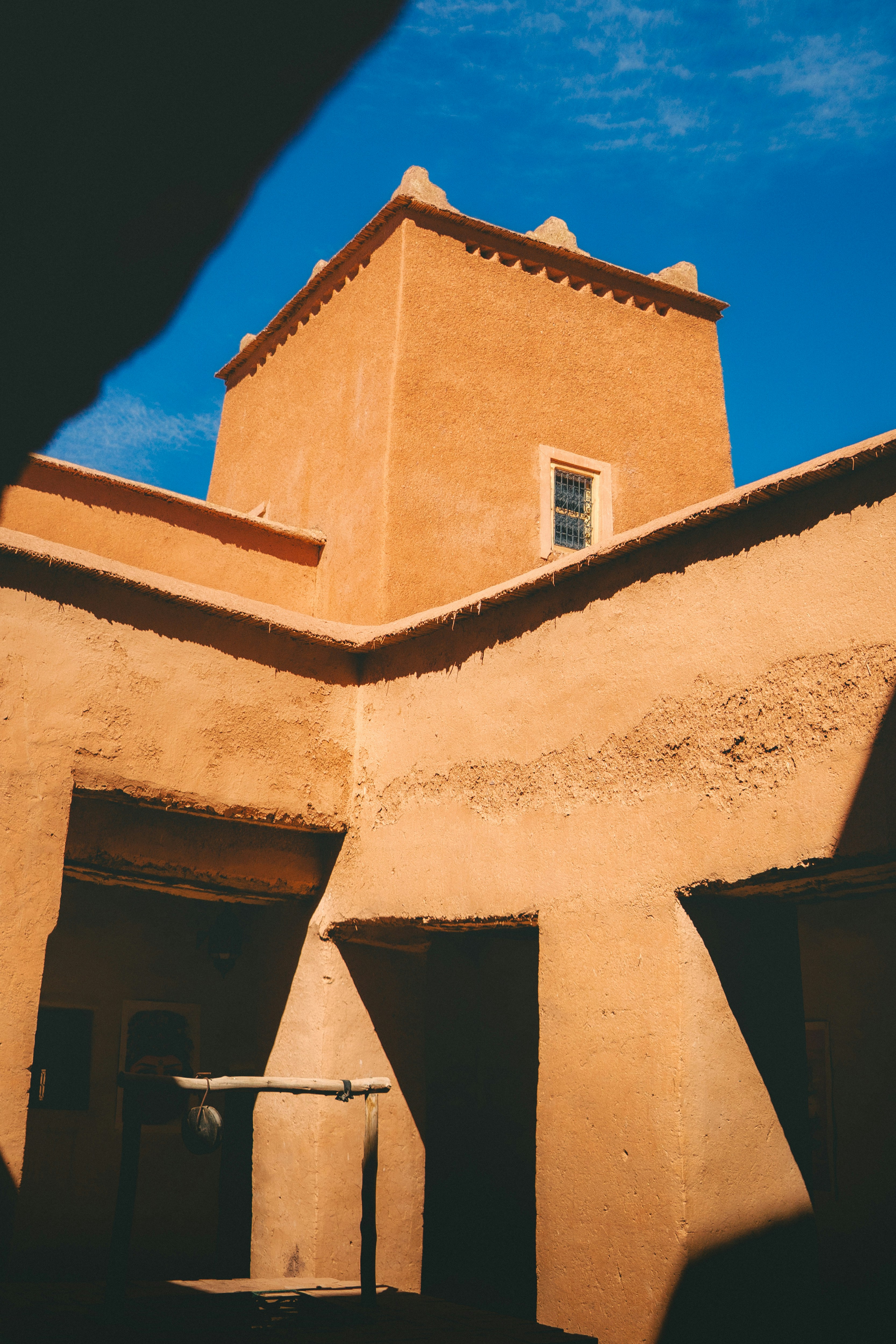Sunlit courtyard of an ancient adobe structure, showcasing textured walls and a distinctive tower against a clear blue sky.