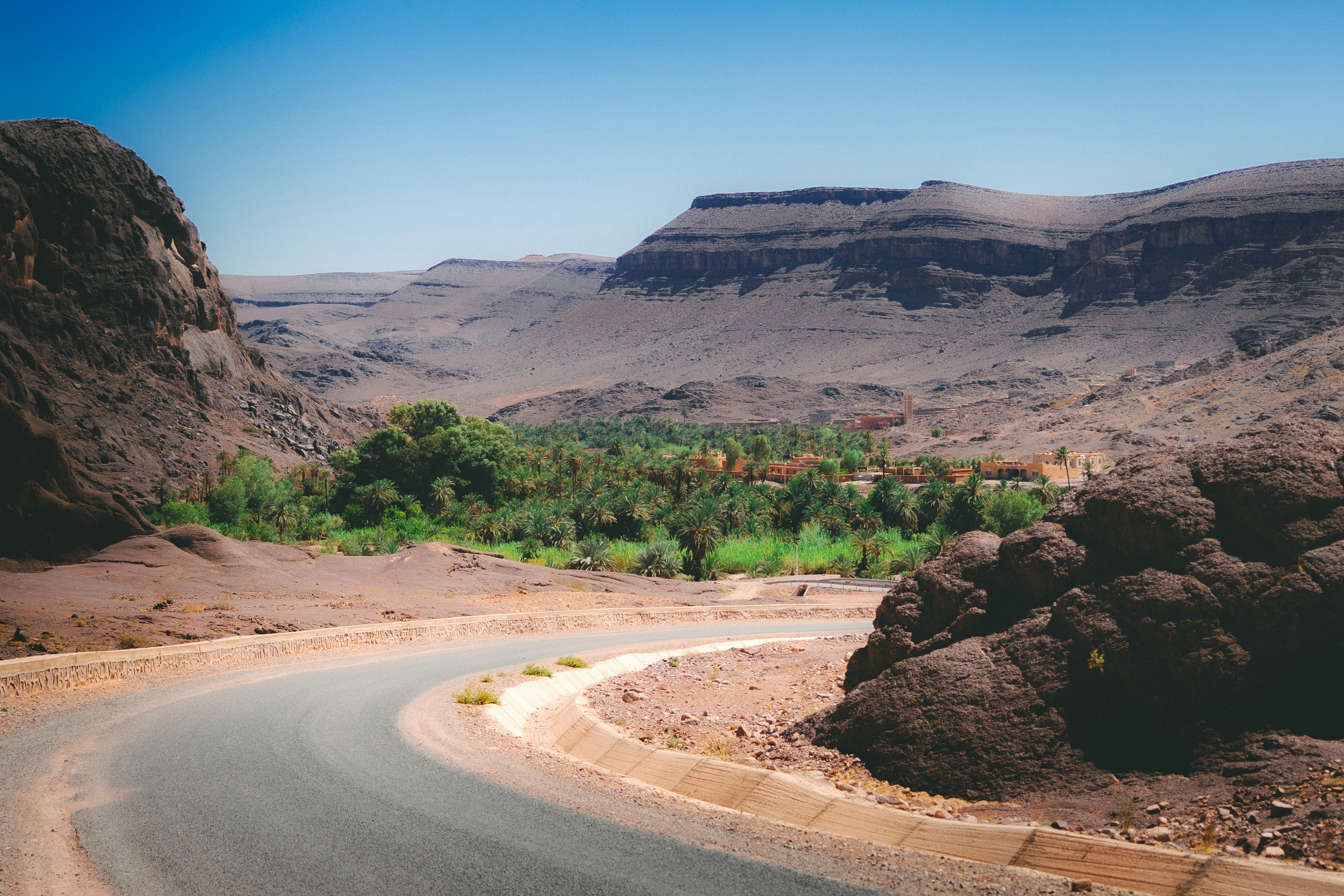 Desert Valley Road curling toward green oasis under basalt cliffs