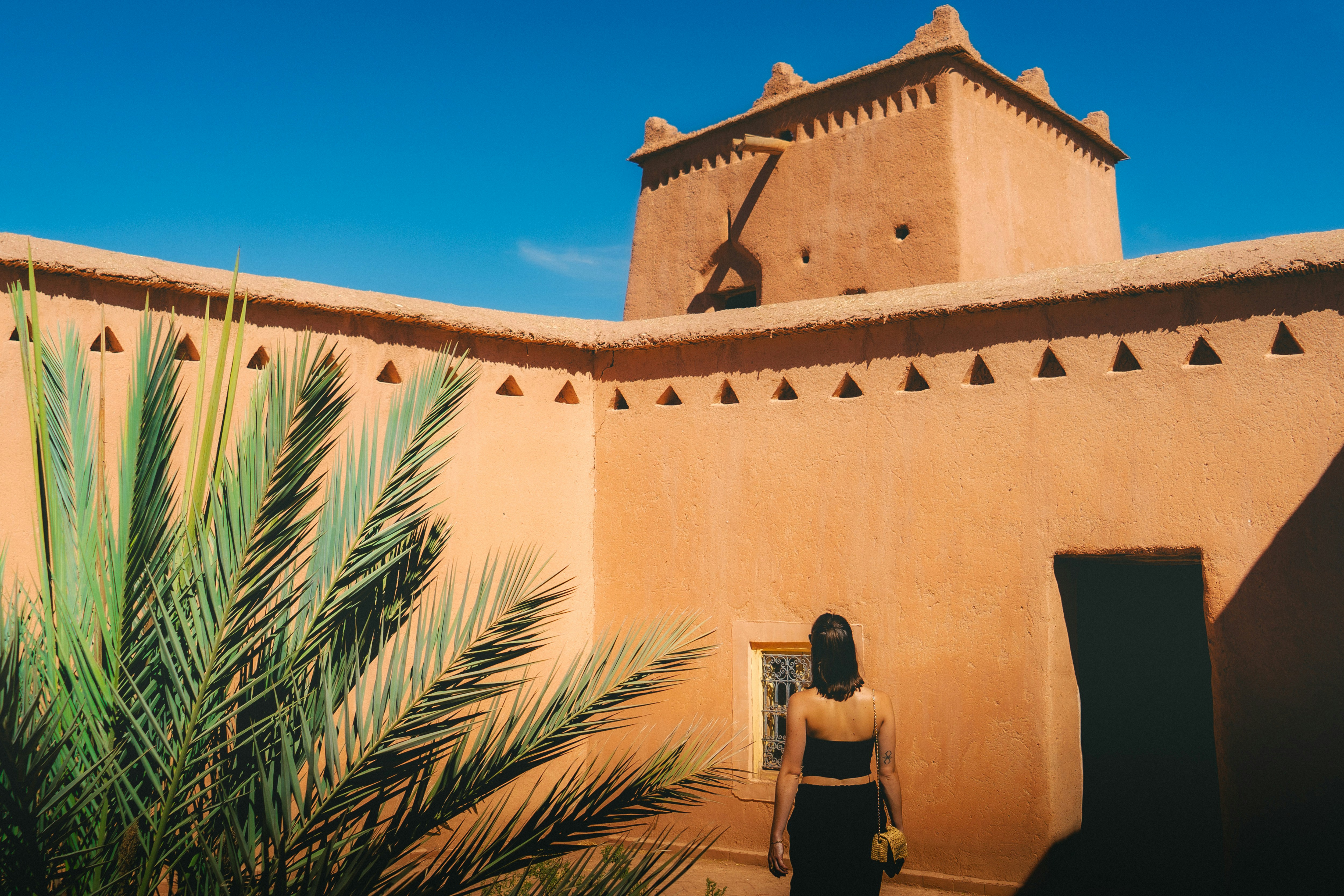 Cobalt Sky over a Sunlit Adobe Wall: A Lone Figure Reaches a Shadowed Door