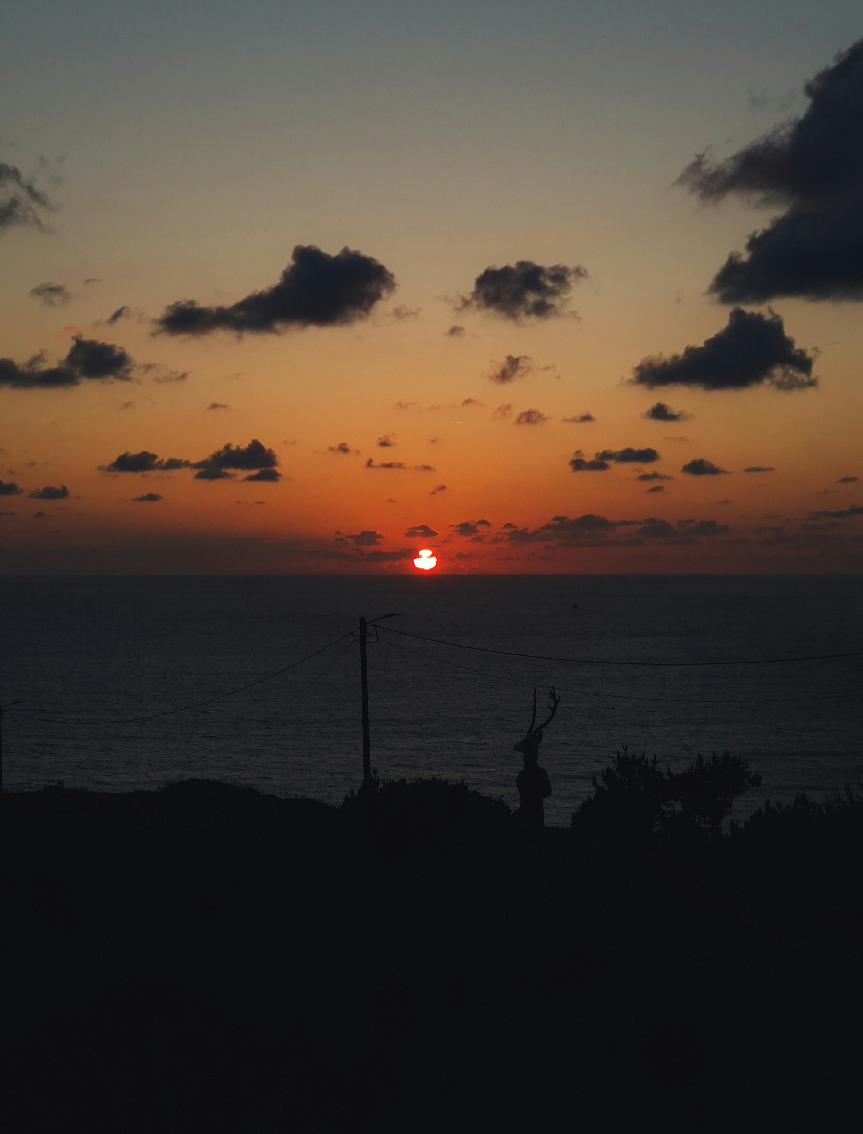 Sunset over the ocean with silhouetted landscape.