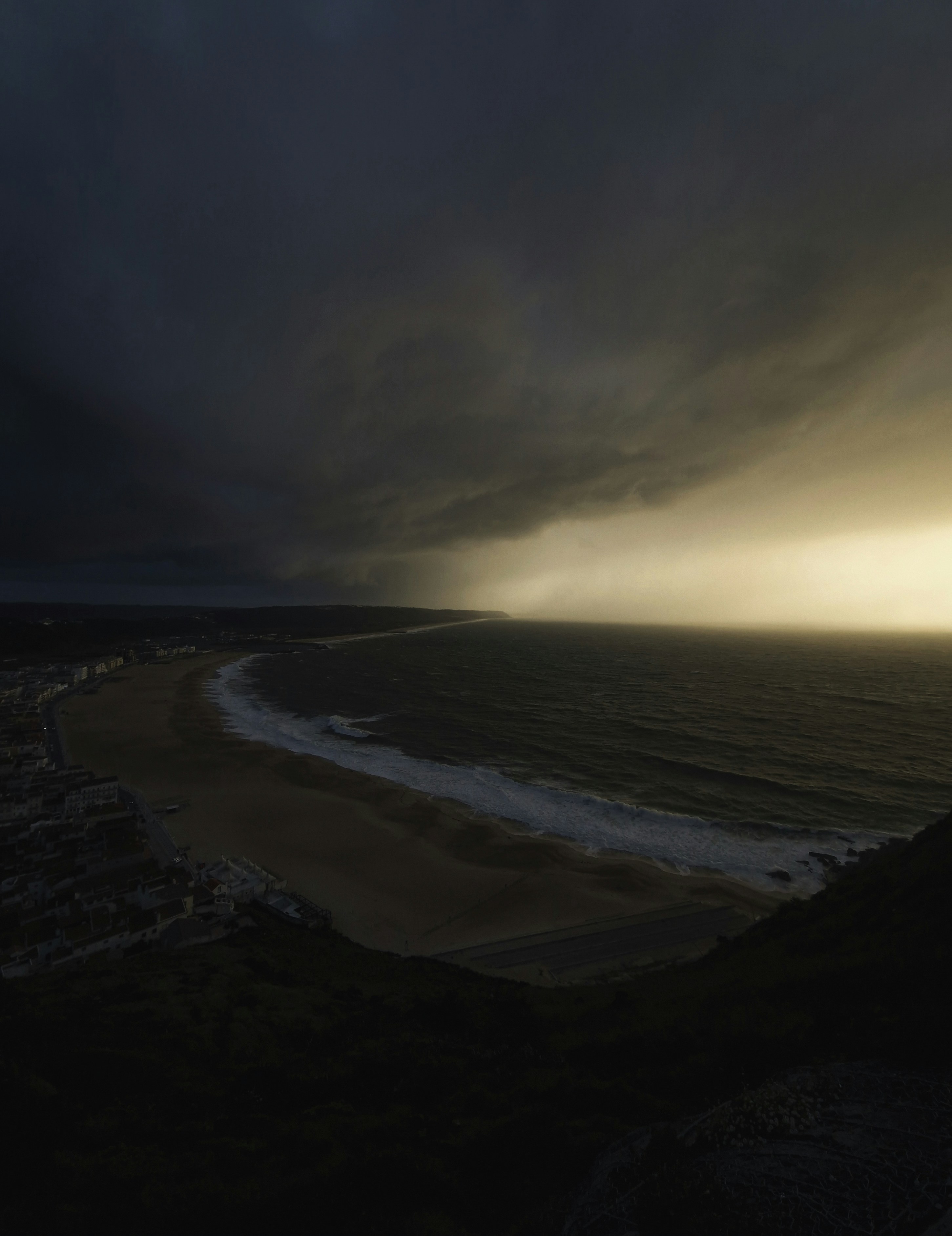 Dark storm clouds over a coastal beach at sunset.