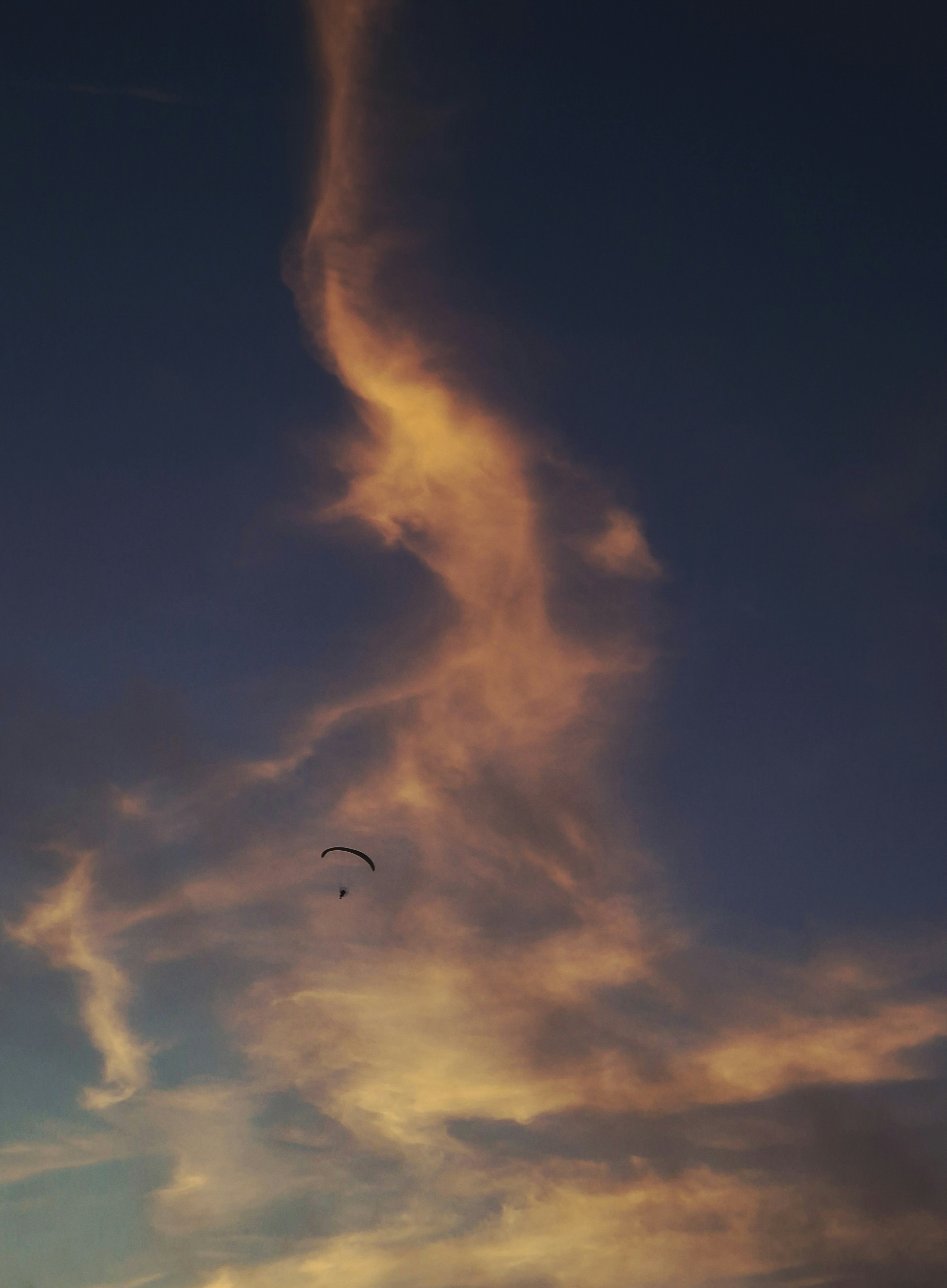 A paraglider soars against a dramatic sunset sky.