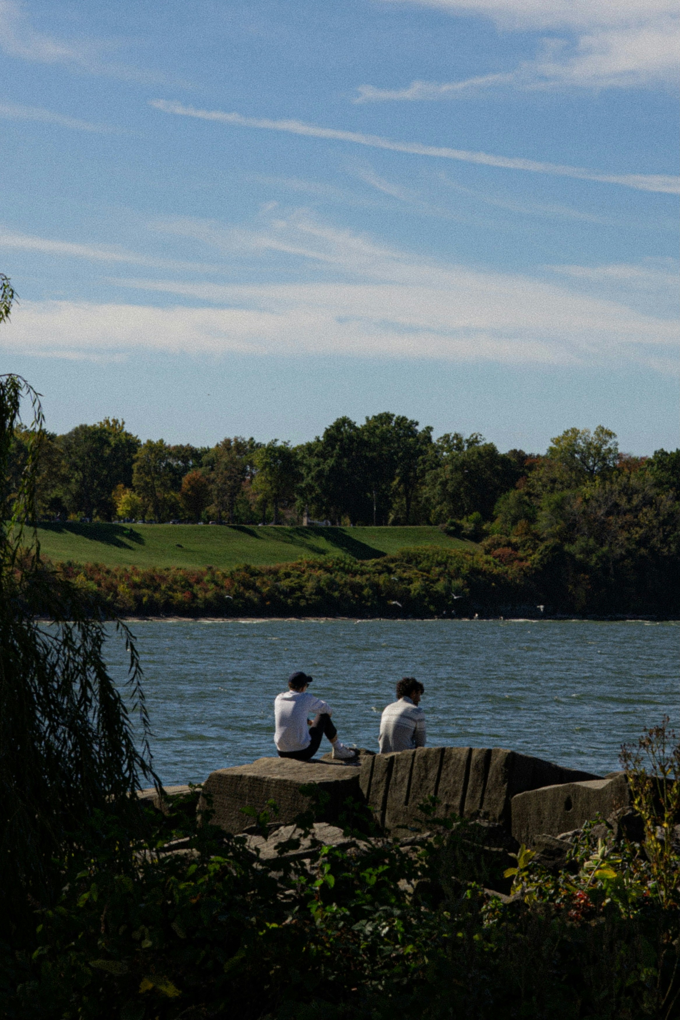 Two people sit on rocks by the water.