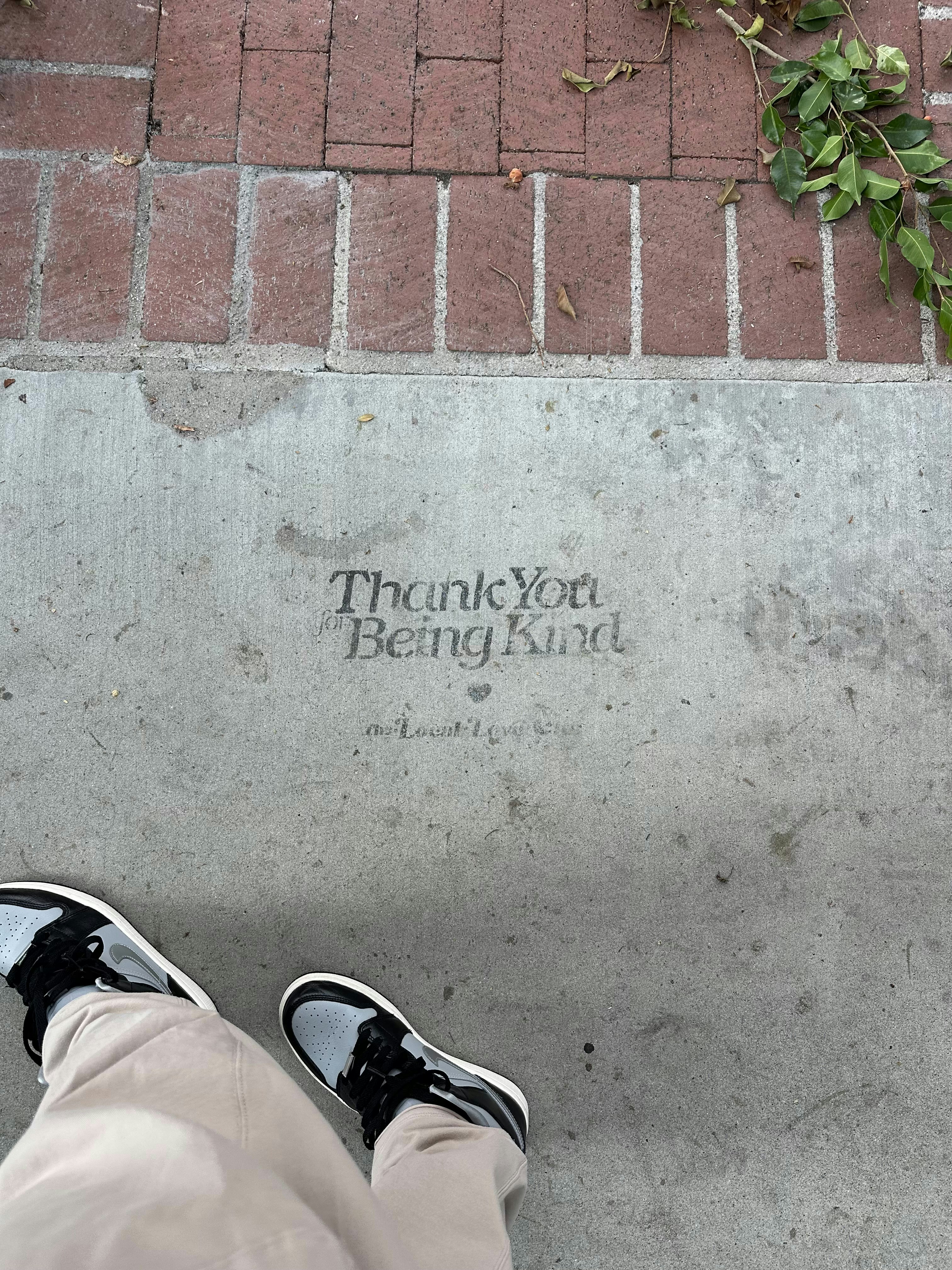 Footwear positioned above a concrete surface with an engraved message expressing gratitude. The scene captures an everyday moment of kindness.