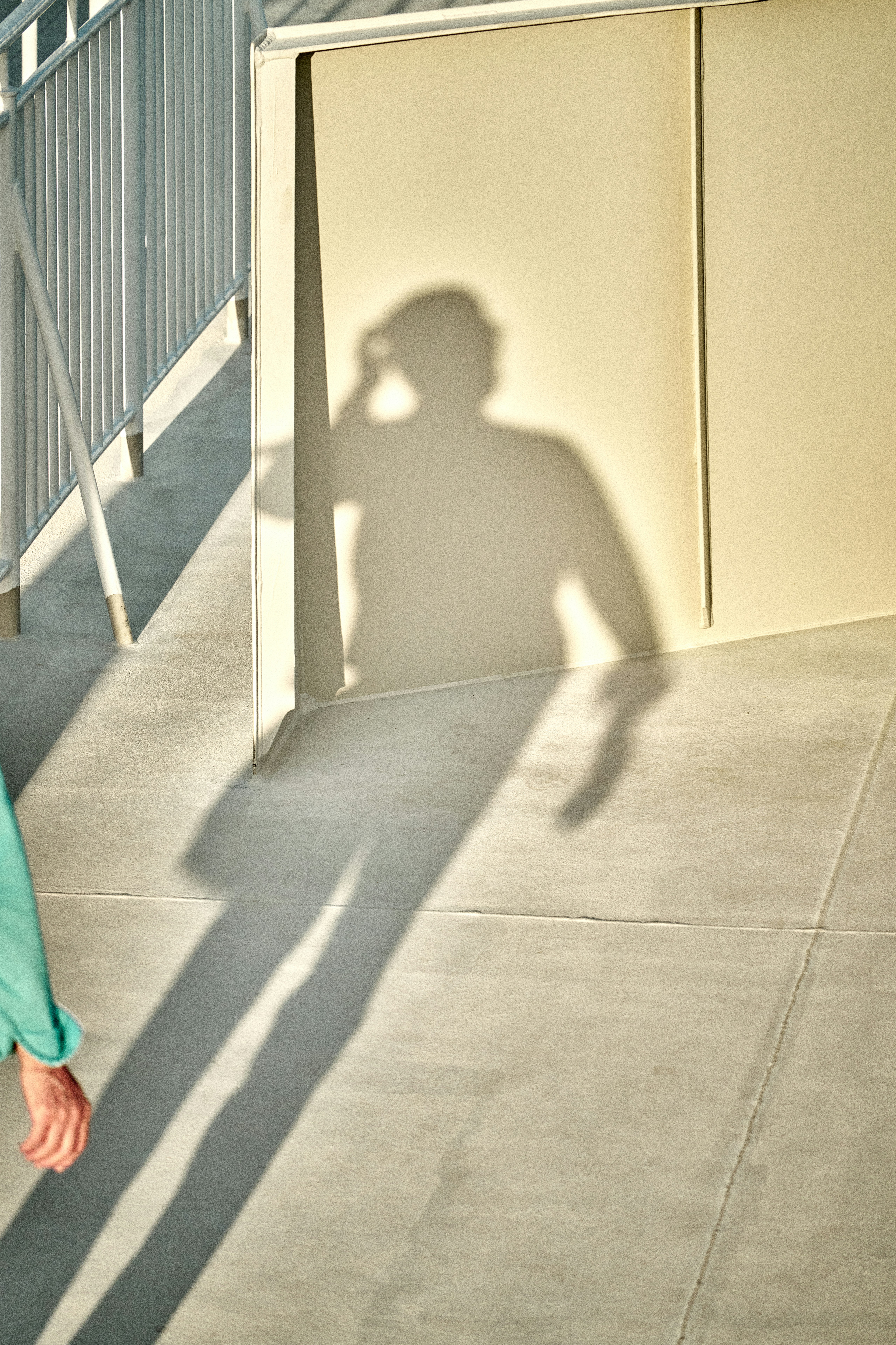 A person's shadow is cast against a light-colored wall, creating an intriguing interplay of light and form. The scene captures a fleeting moment of contemplation.