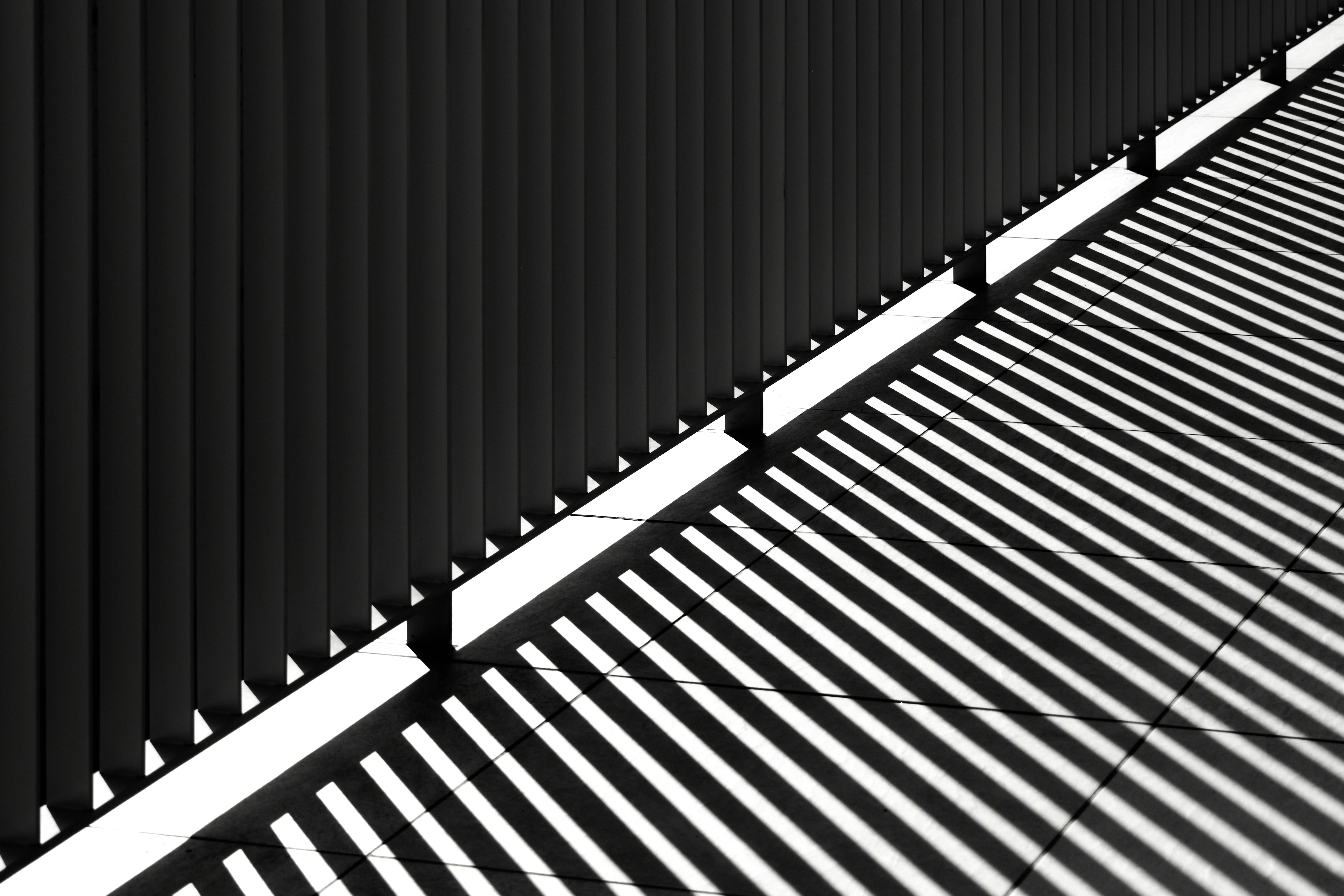 Abstract composition of vertical slats casting intricate shadows on a surface, emphasizing contrast and form.