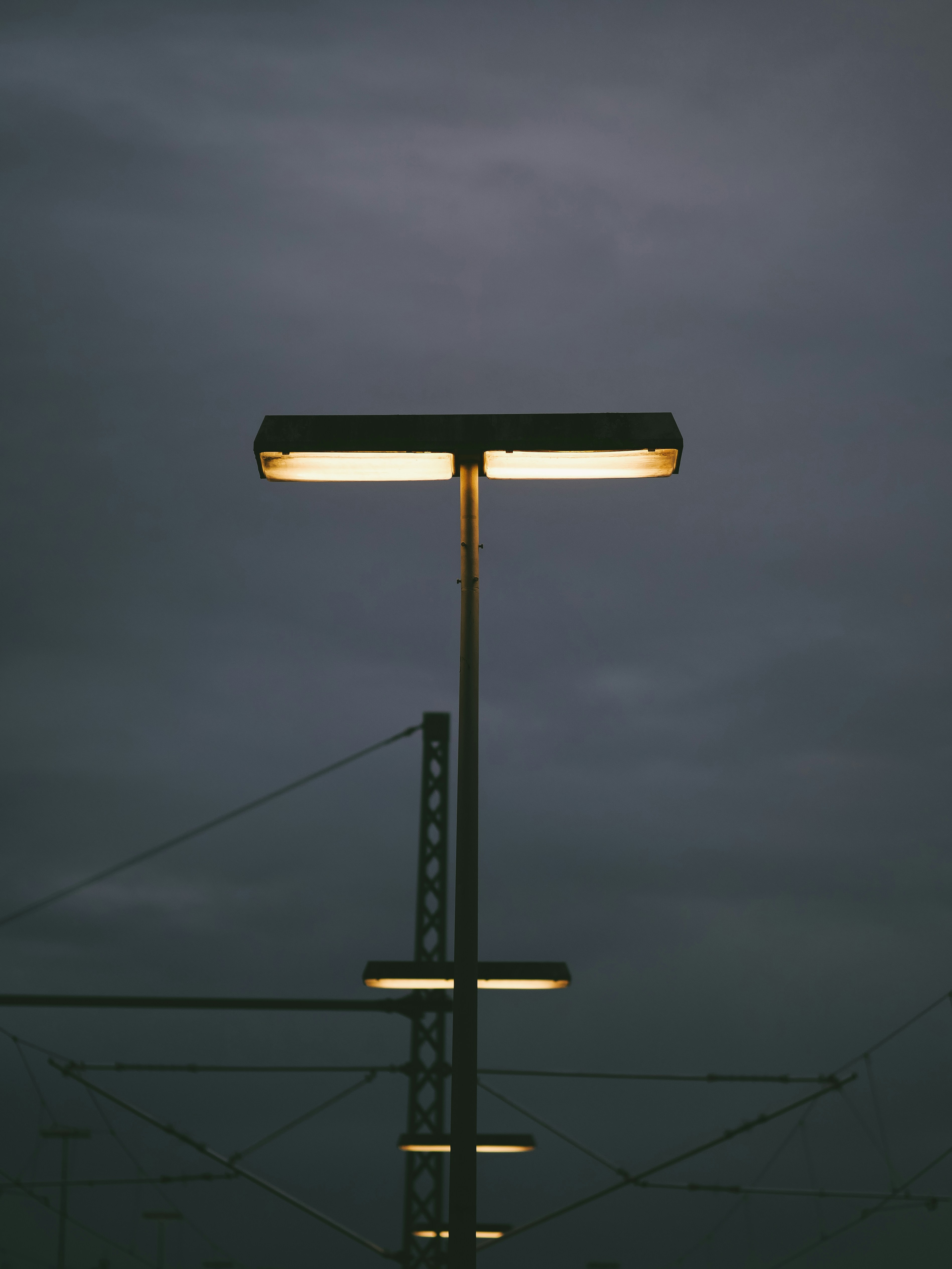 Street lamps glowing against a moody sky, casting a warm light amidst the cool tones of twilight.