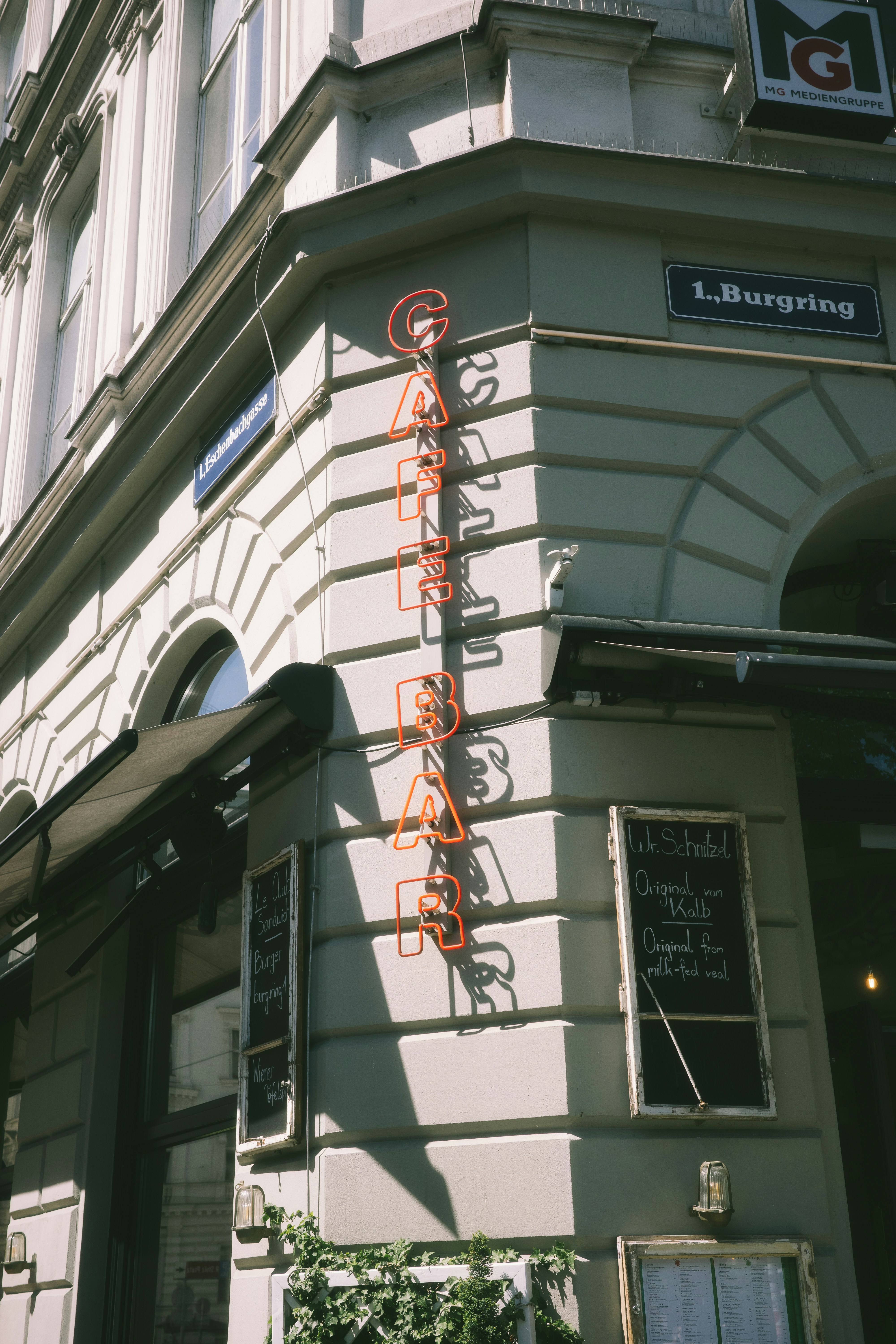 Neon sign displaying 'Café Bar' on a charming building corner, complemented by chalkboard menus showcasing local dishes.