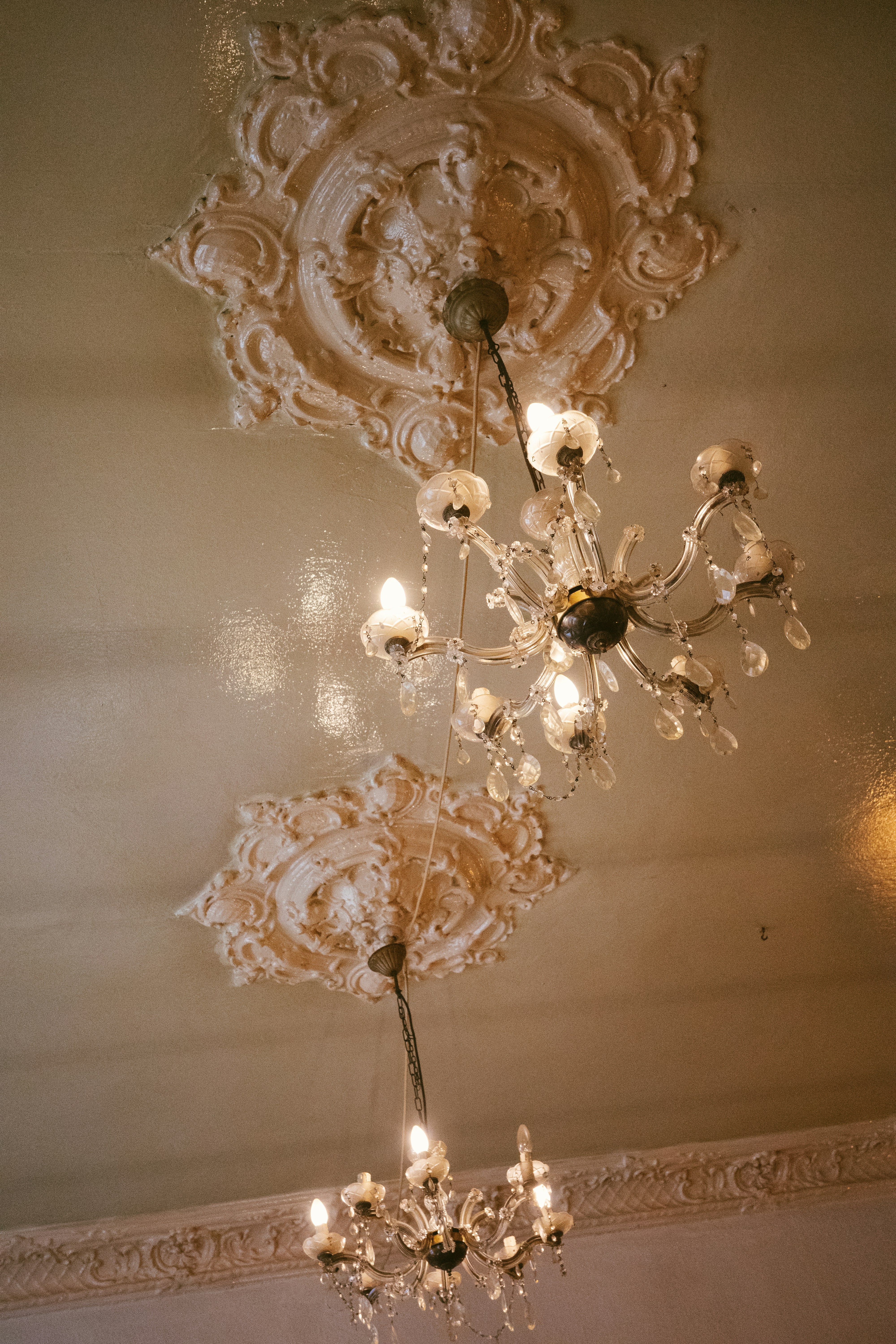 Ornate ceiling with intricate plasterwork featuring two elegant chandeliers casting warm light. 