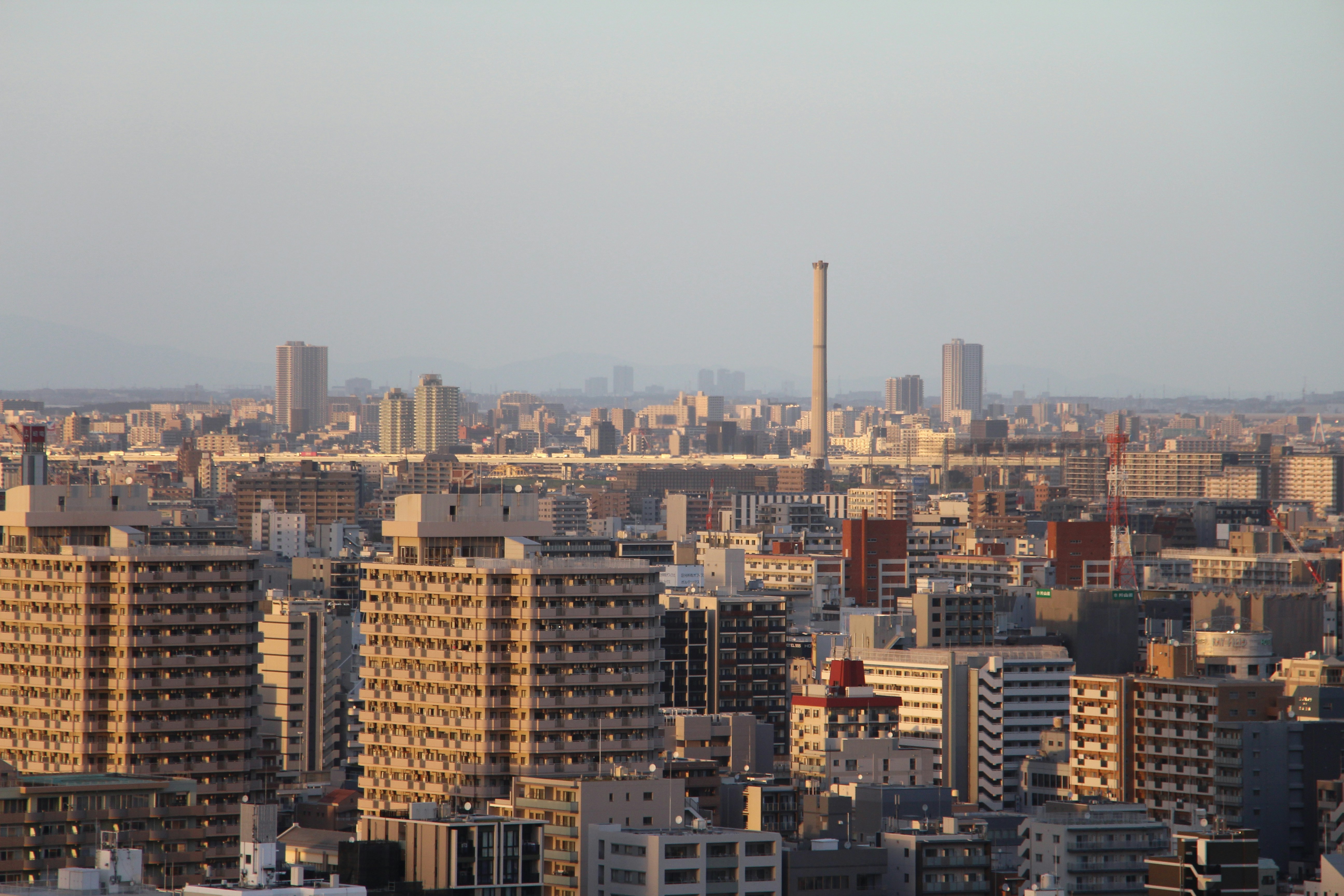 A panoramic view of a bustling cityscape at dusk, showcasing a blend of high-rise buildings and industrial structures against a fading sky.