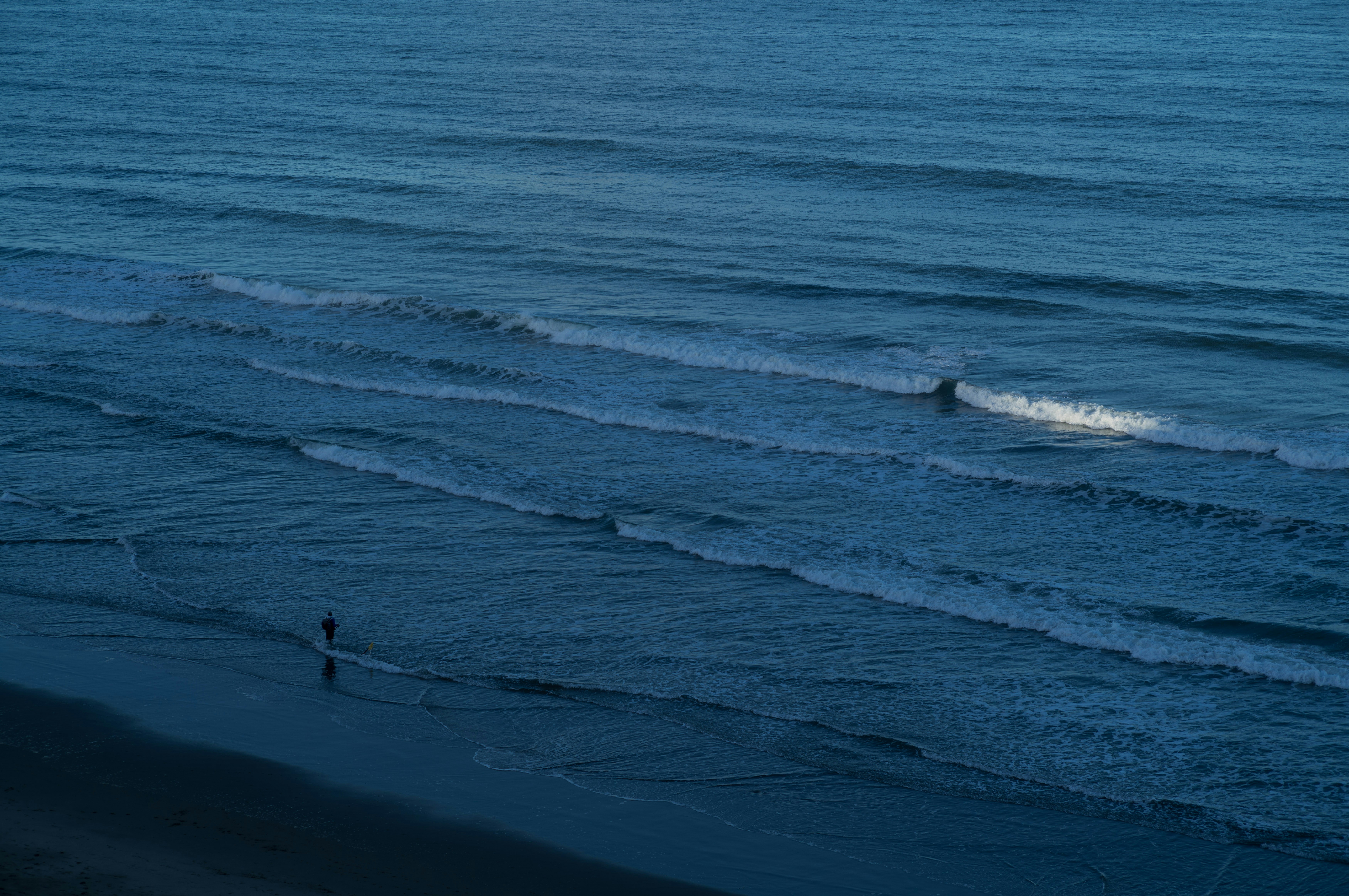 A man facing the waves of Pacific Ocean, San Francisco. | Surfer catches a wave near a sandy beach.