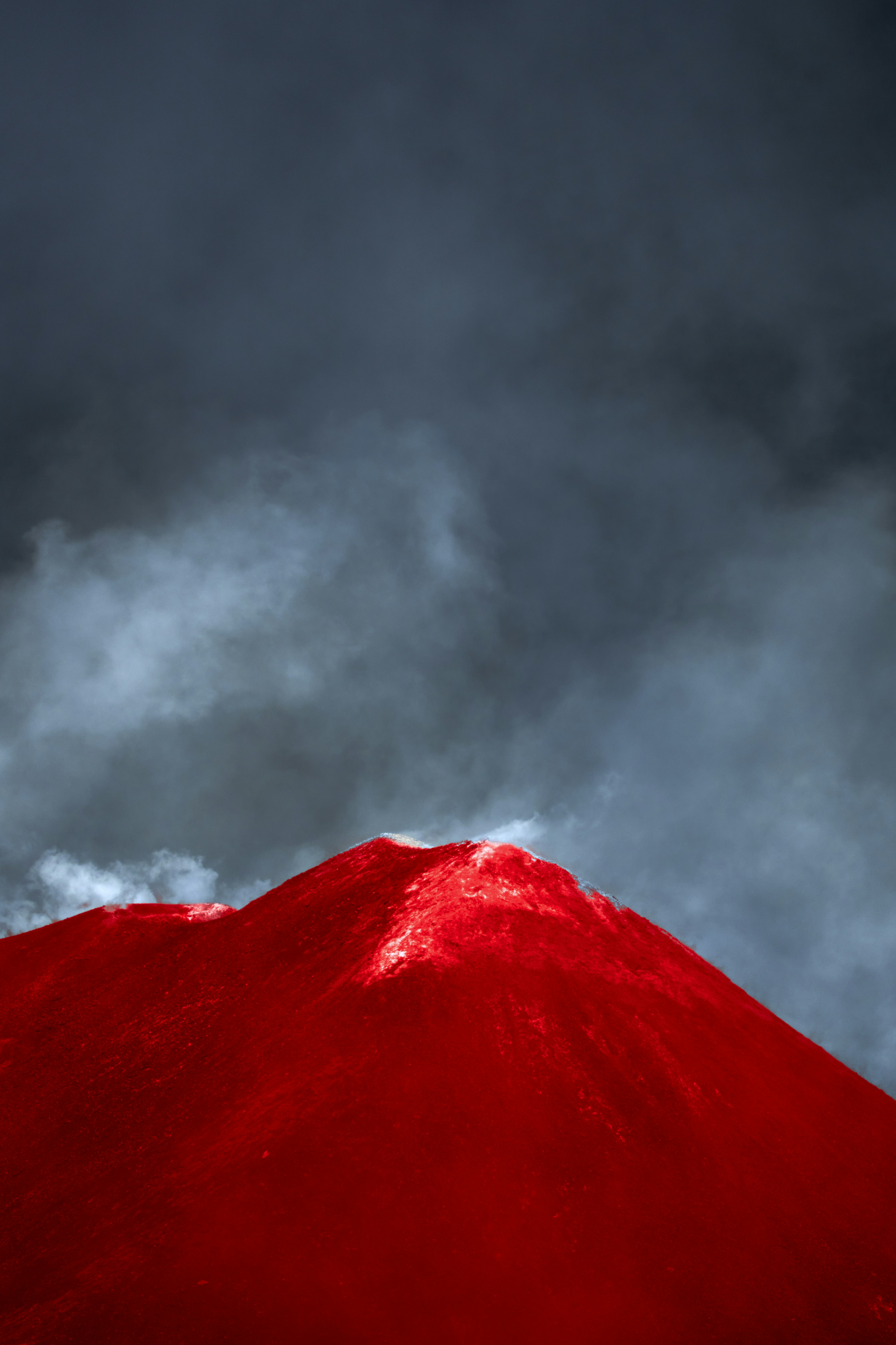 Vibrant red volcanic peak under a dramatic sky, shrouded in swirling mist. The scene captures the raw power of nature.