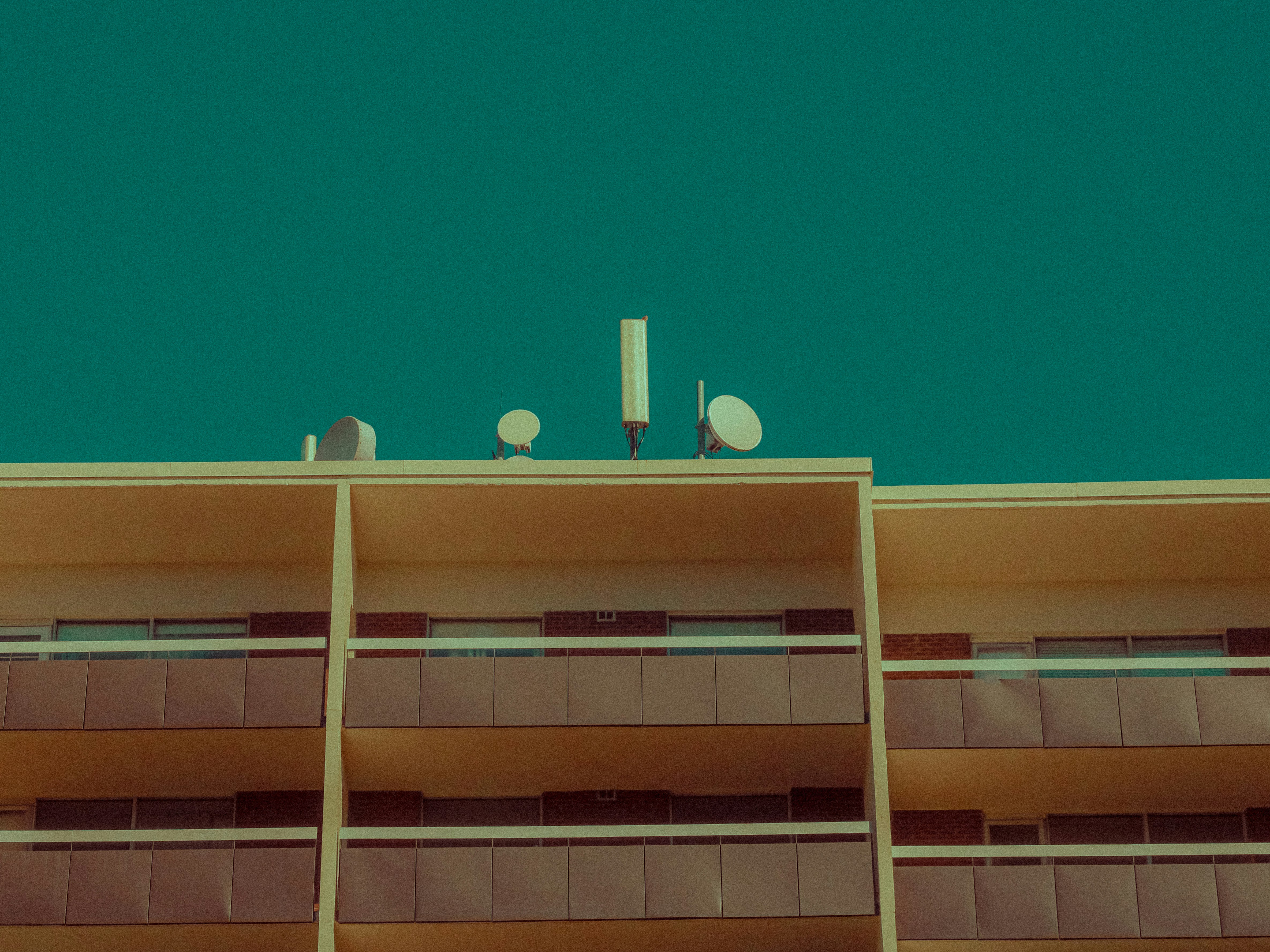 quaint apartment building under clear blue sky | Modern apartment building with balconies and antennas