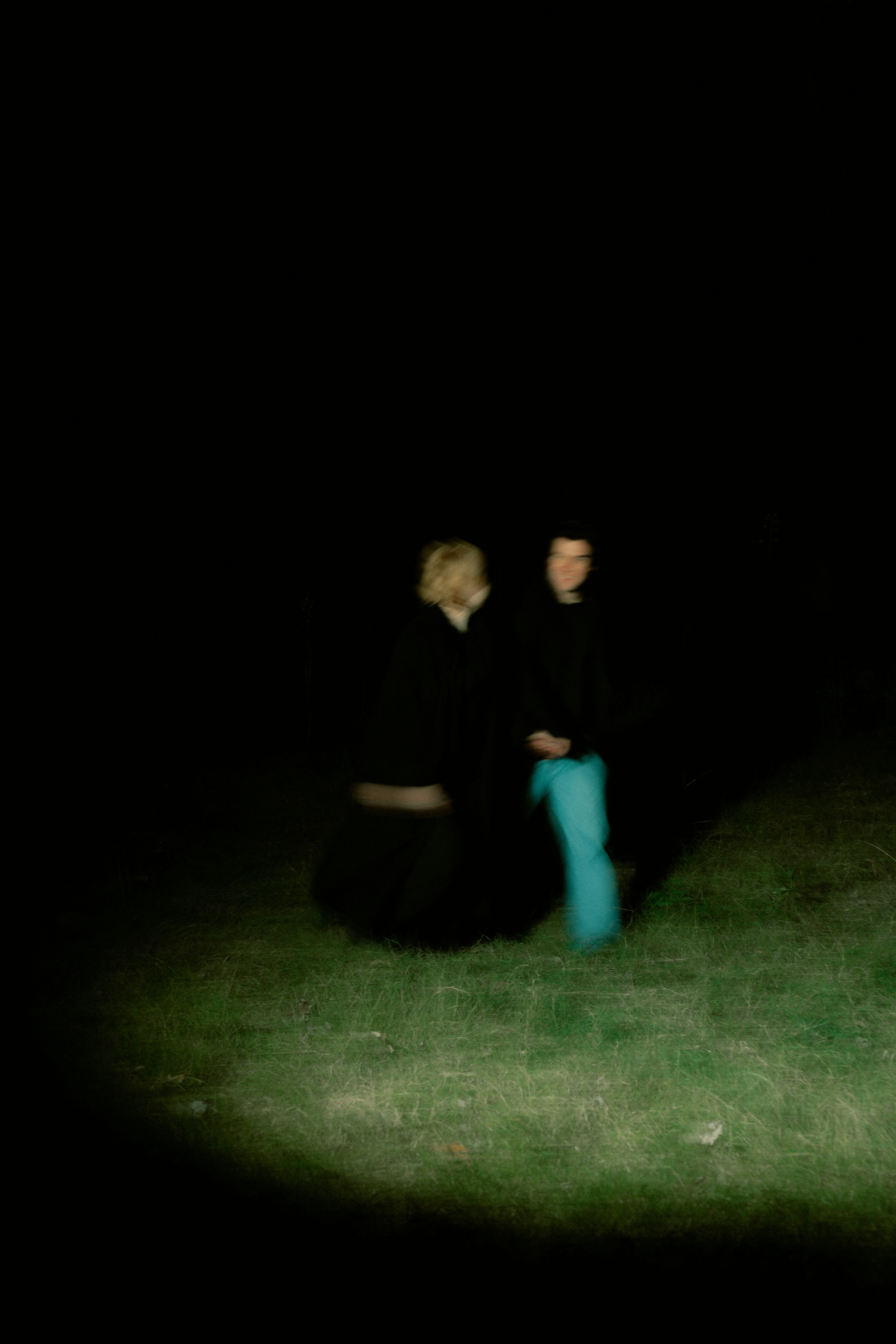 Two people standing in a dark grassy field.