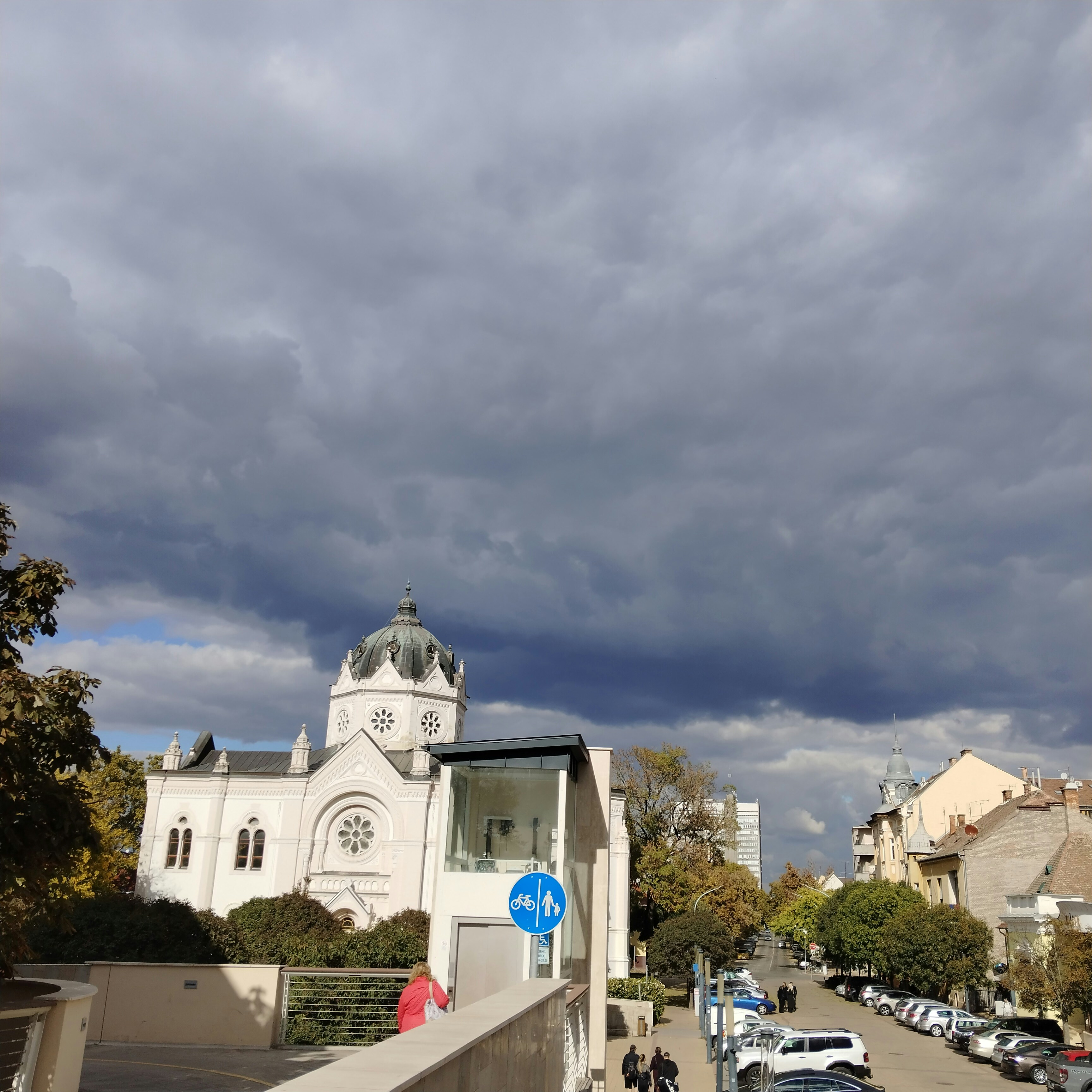 Historic church nestled among modern architecture under a dramatic sky, showcasing a blend of old and new urban landscapes.
