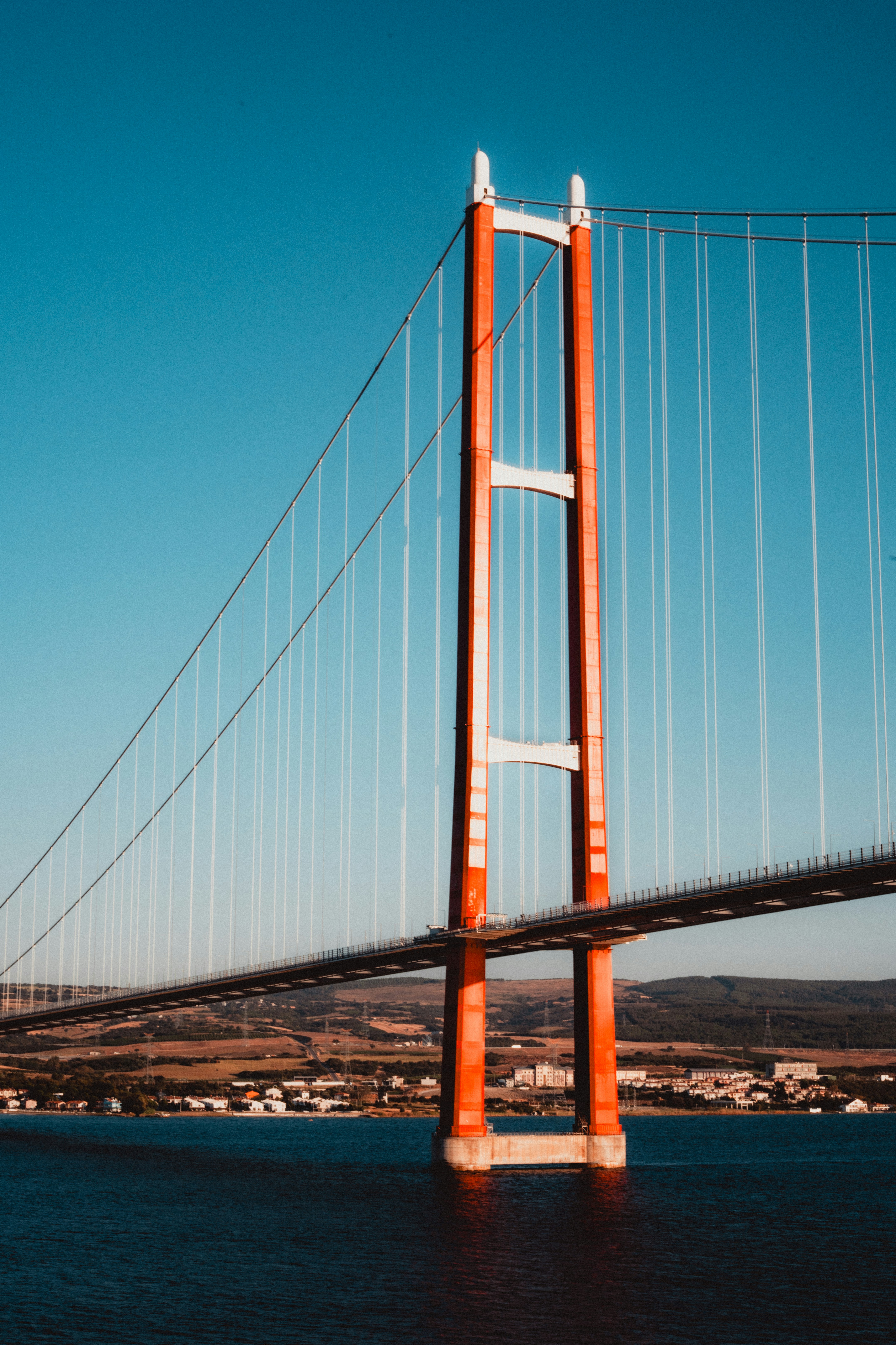 Red suspension bridge tower over blue water.