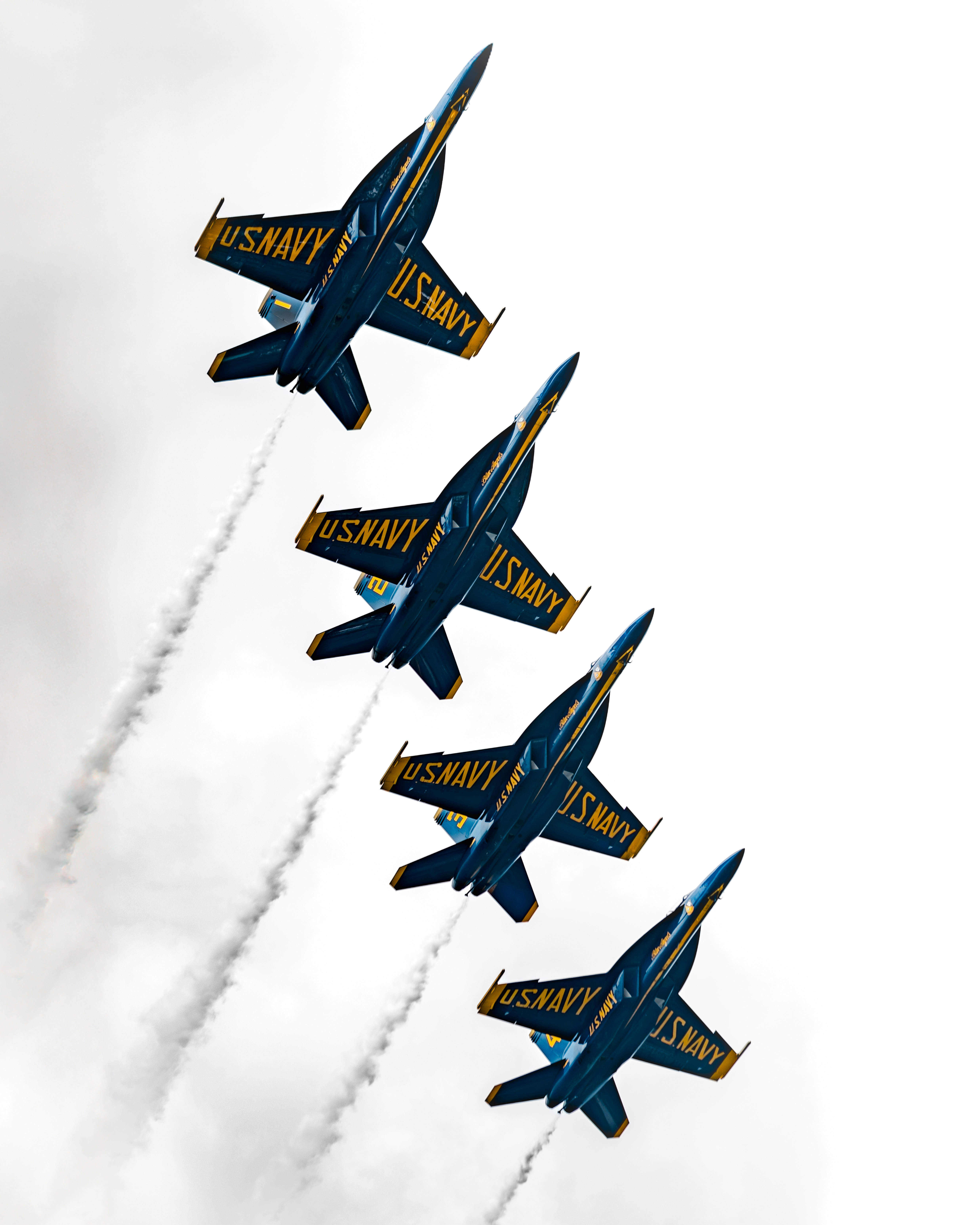 Four U.S. Navy fighter jets executing a synchronized maneuver against a cloudy backdrop.