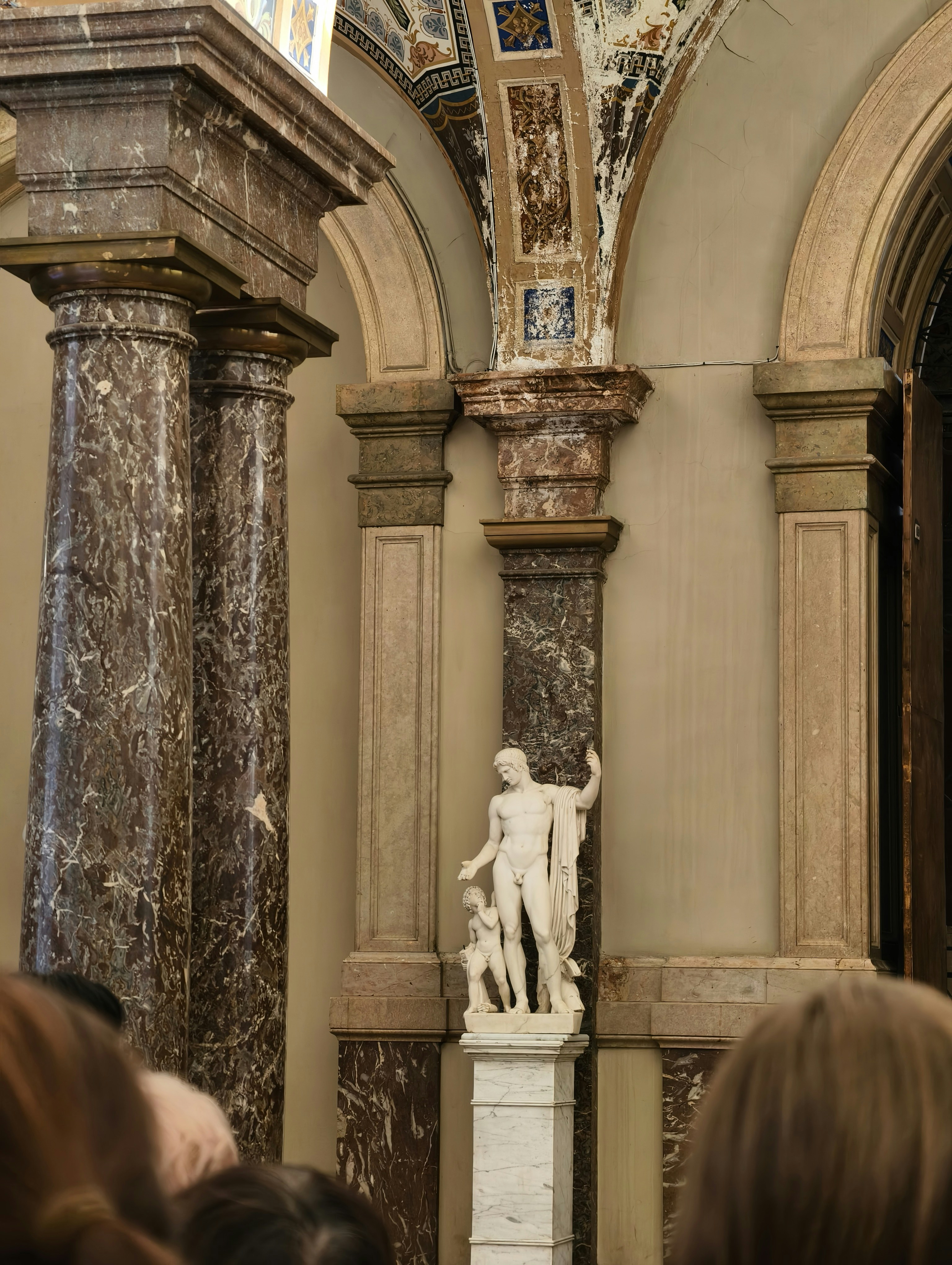 A marble statue depicting a historical figure stands beside ornate columns in a grand architectural space, highlighting the contrast between art and structure.