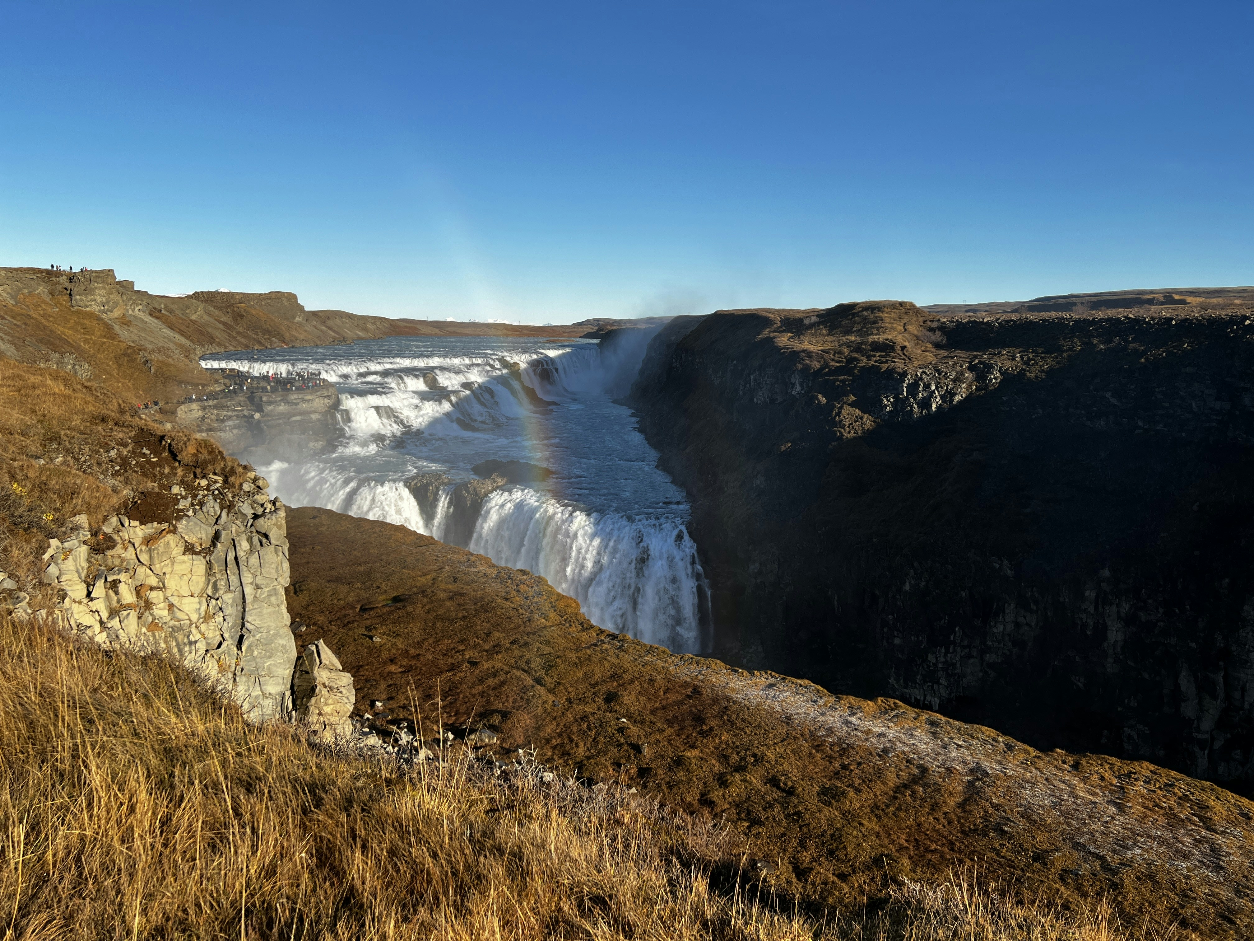 Majestic waterfall cascading into a deep gorge, illuminated by sunlight creating a subtle rainbow effect.
