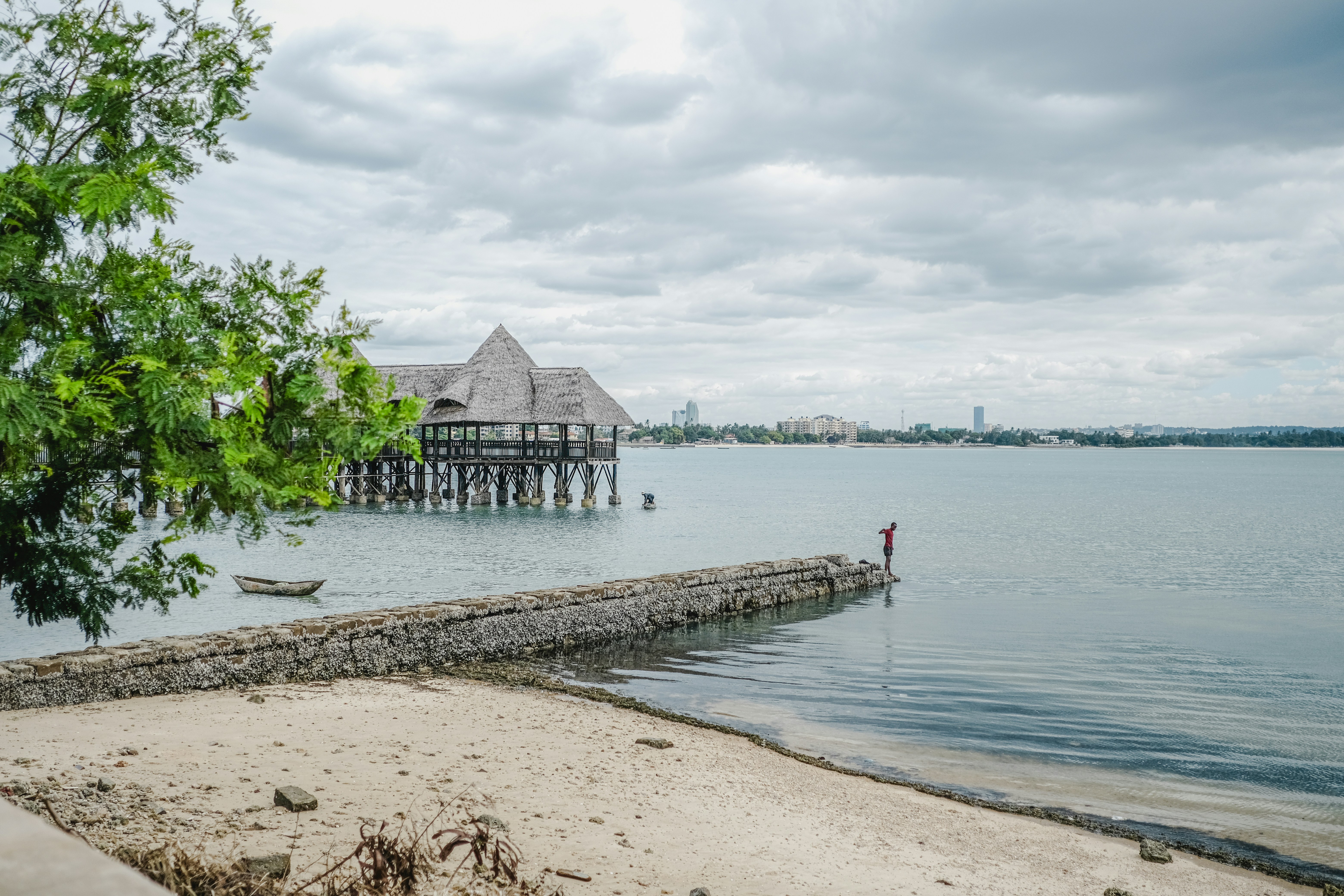 Lone Angler at the End of a Wooden Jetty with Thatched Huts and a Distant Skyline