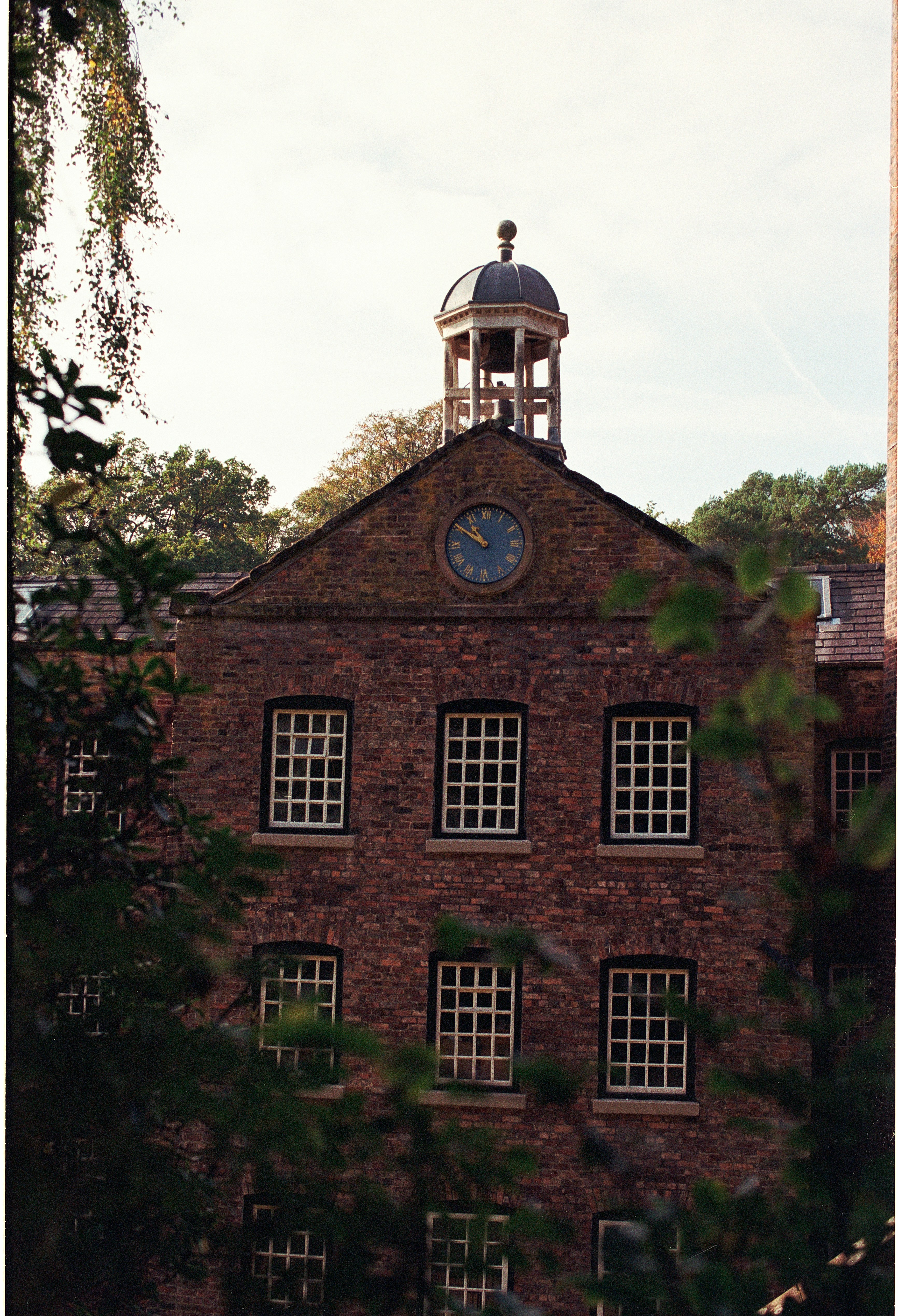 Historic brick building with a clock tower, framed by lush greenery, showcasing classic architectural details.
