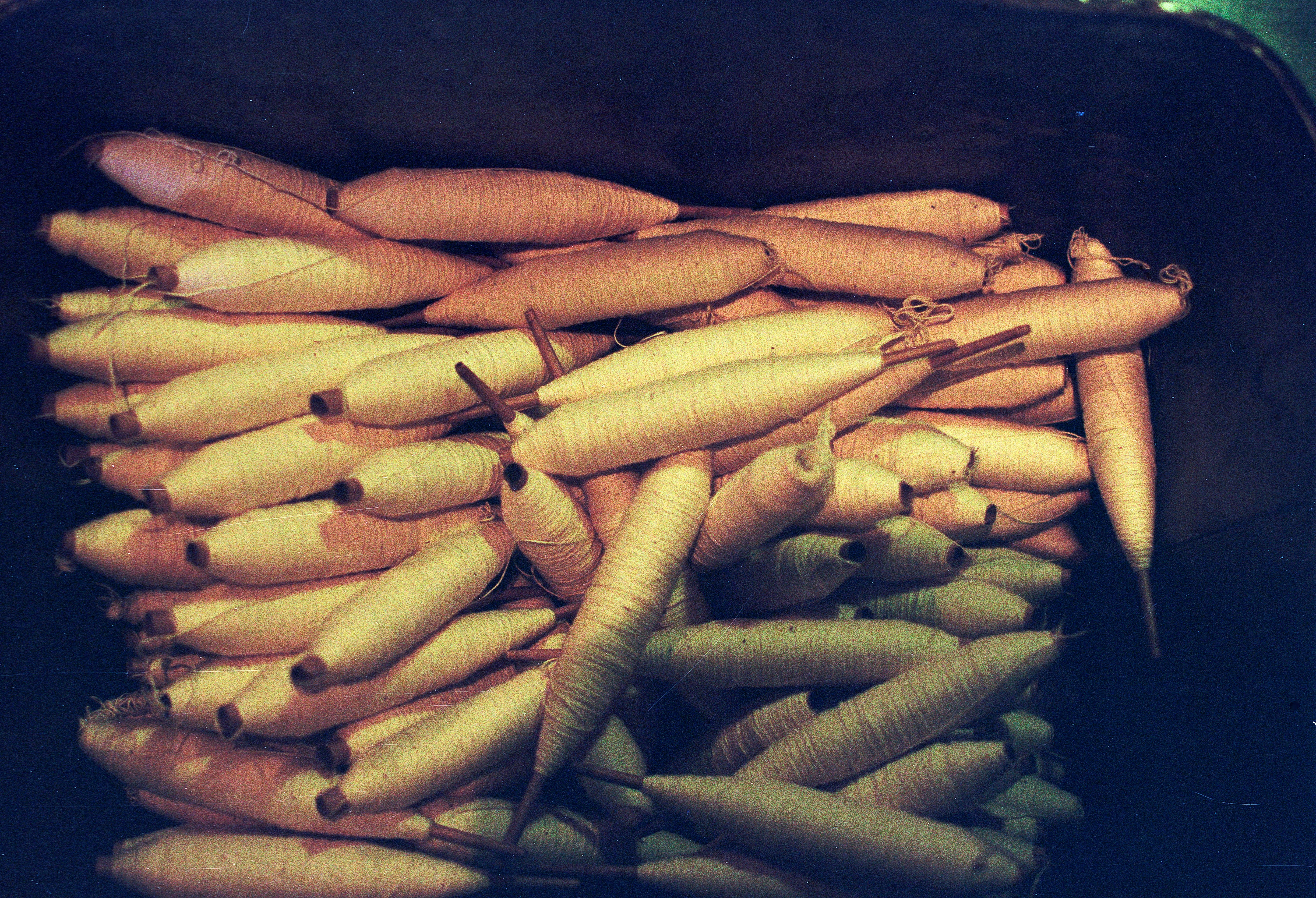A collection of spools filled with thread, arranged in a wooden container, showcasing craftsmanship and color variations.