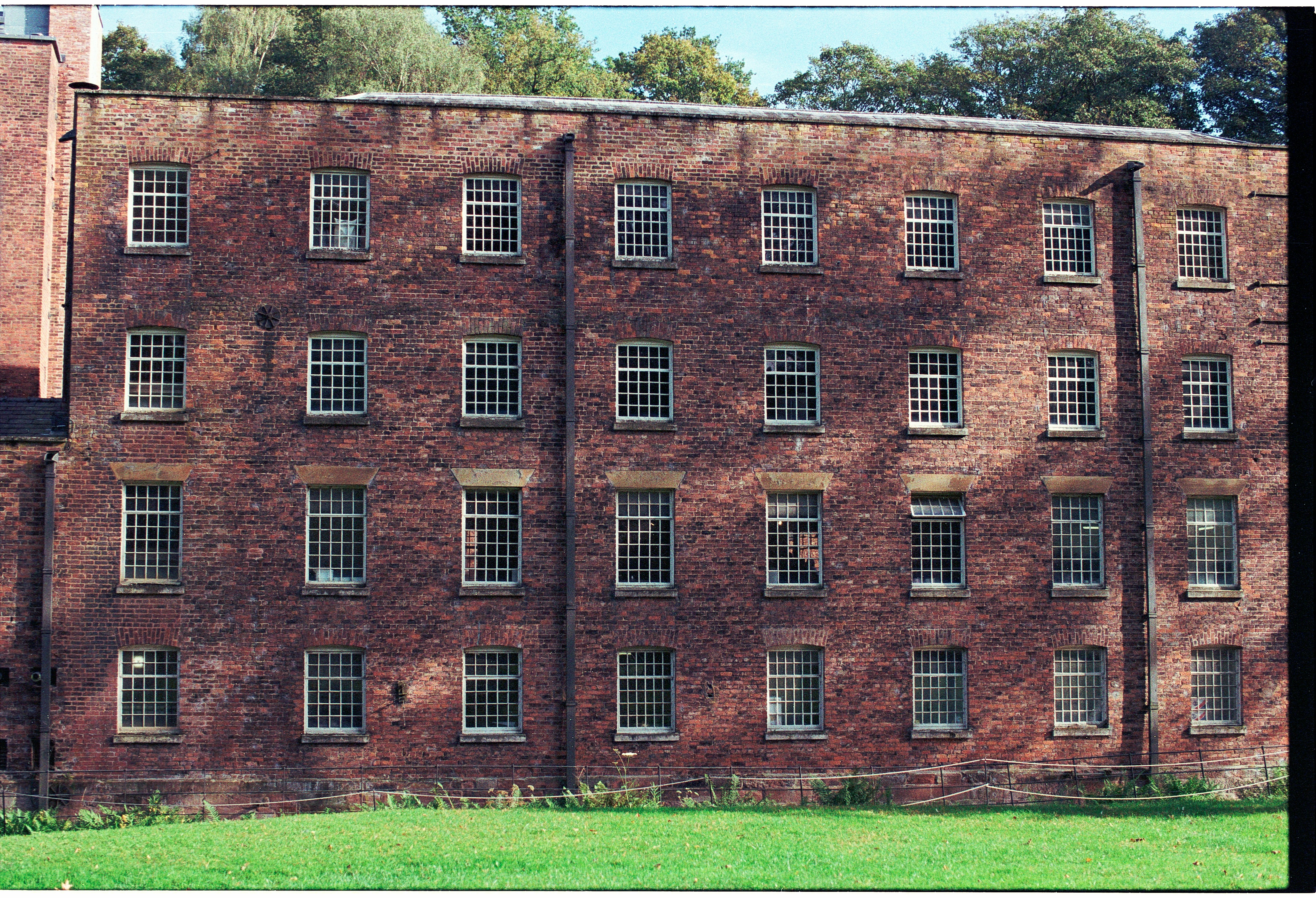 Brick wall of a historic building featuring multiple windows and a green lawn in front, showcasing architectural details and textures.