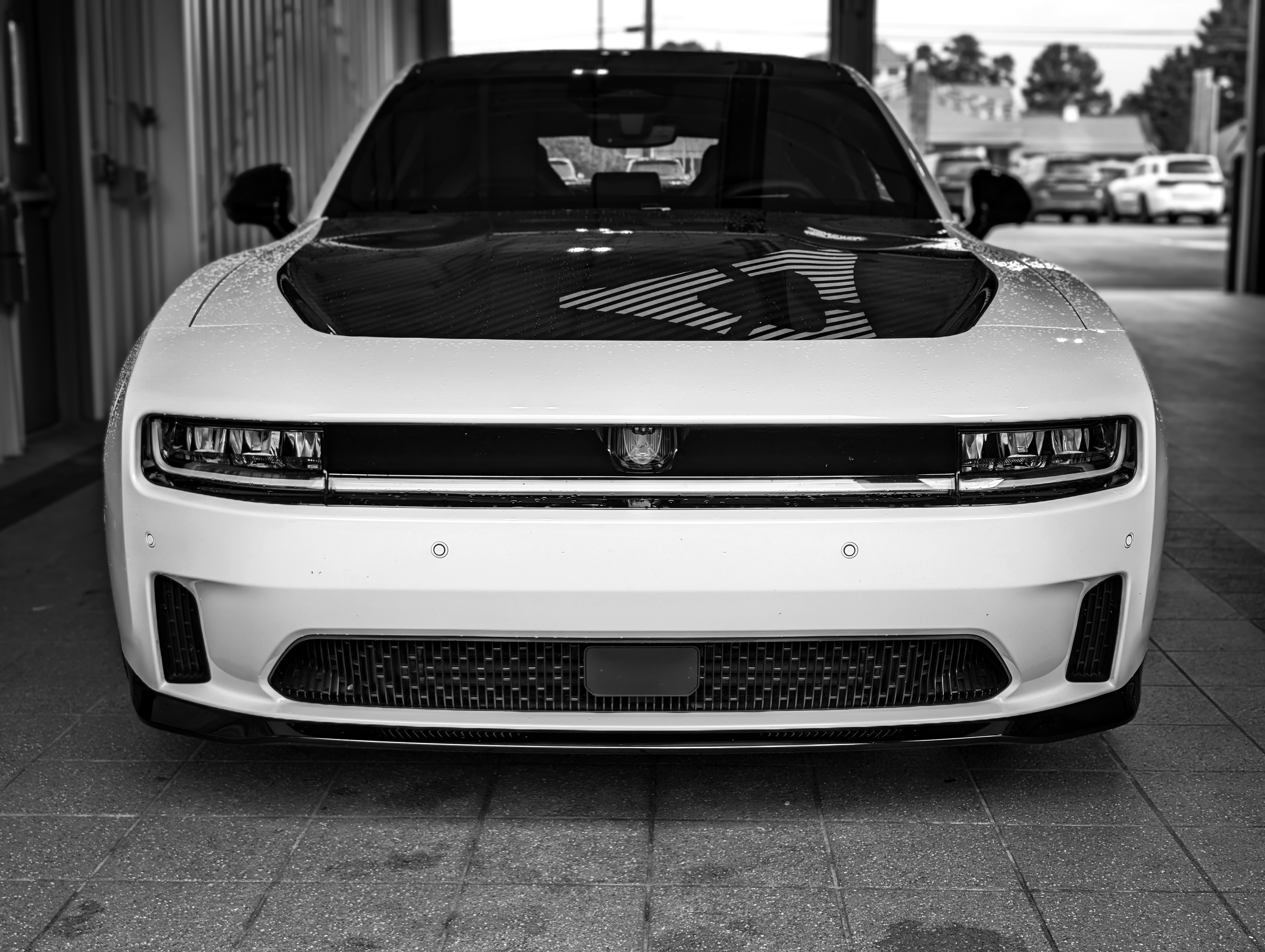 Sleek white sports car with a glossy black hood, positioned in a garage setting. The front view emphasizes its aggressive design and modern aesthetics.