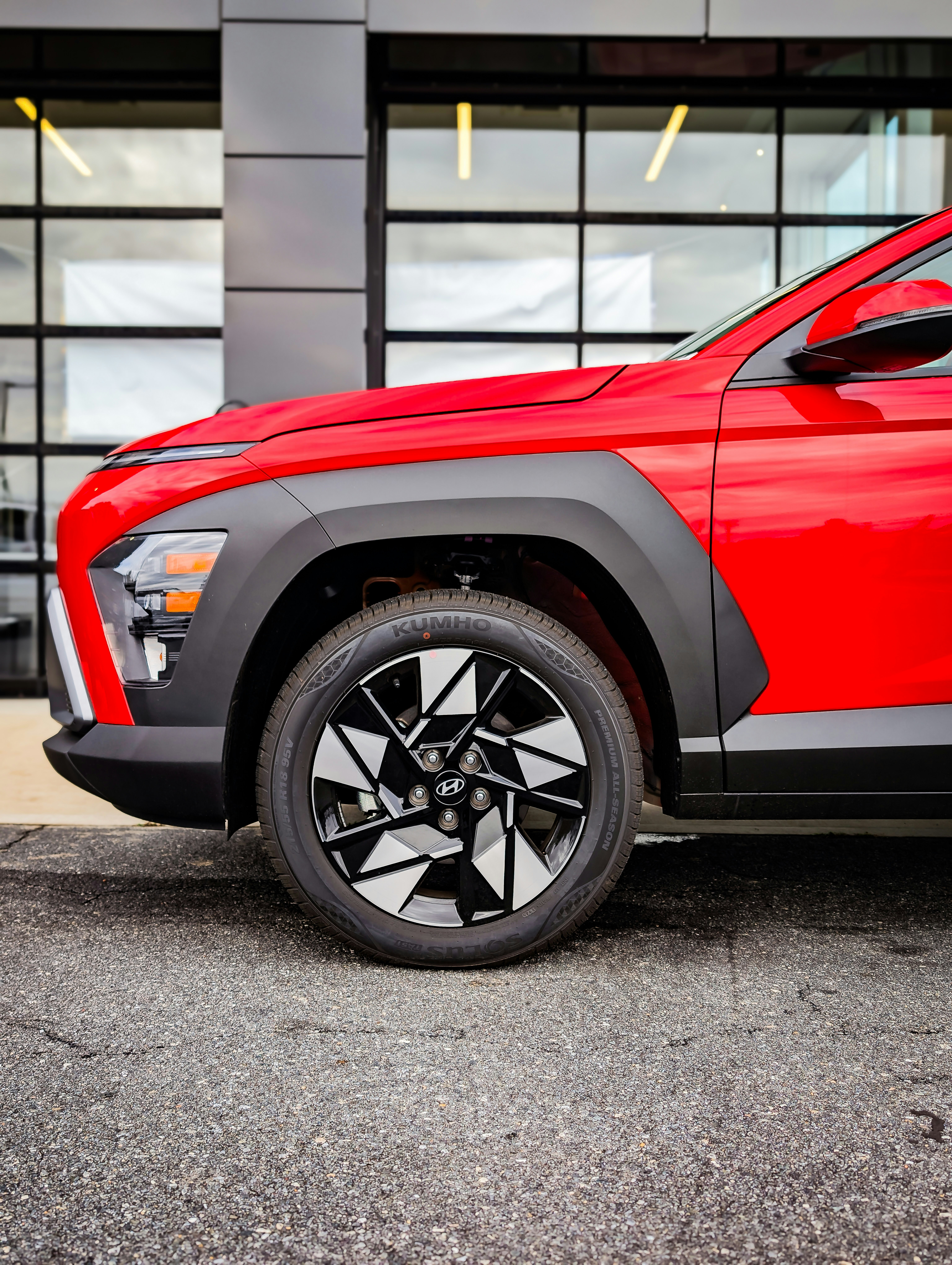 Close-up view of a red vehicle showcasing its sleek wheel design and bold body lines against a backdrop of glass architecture.