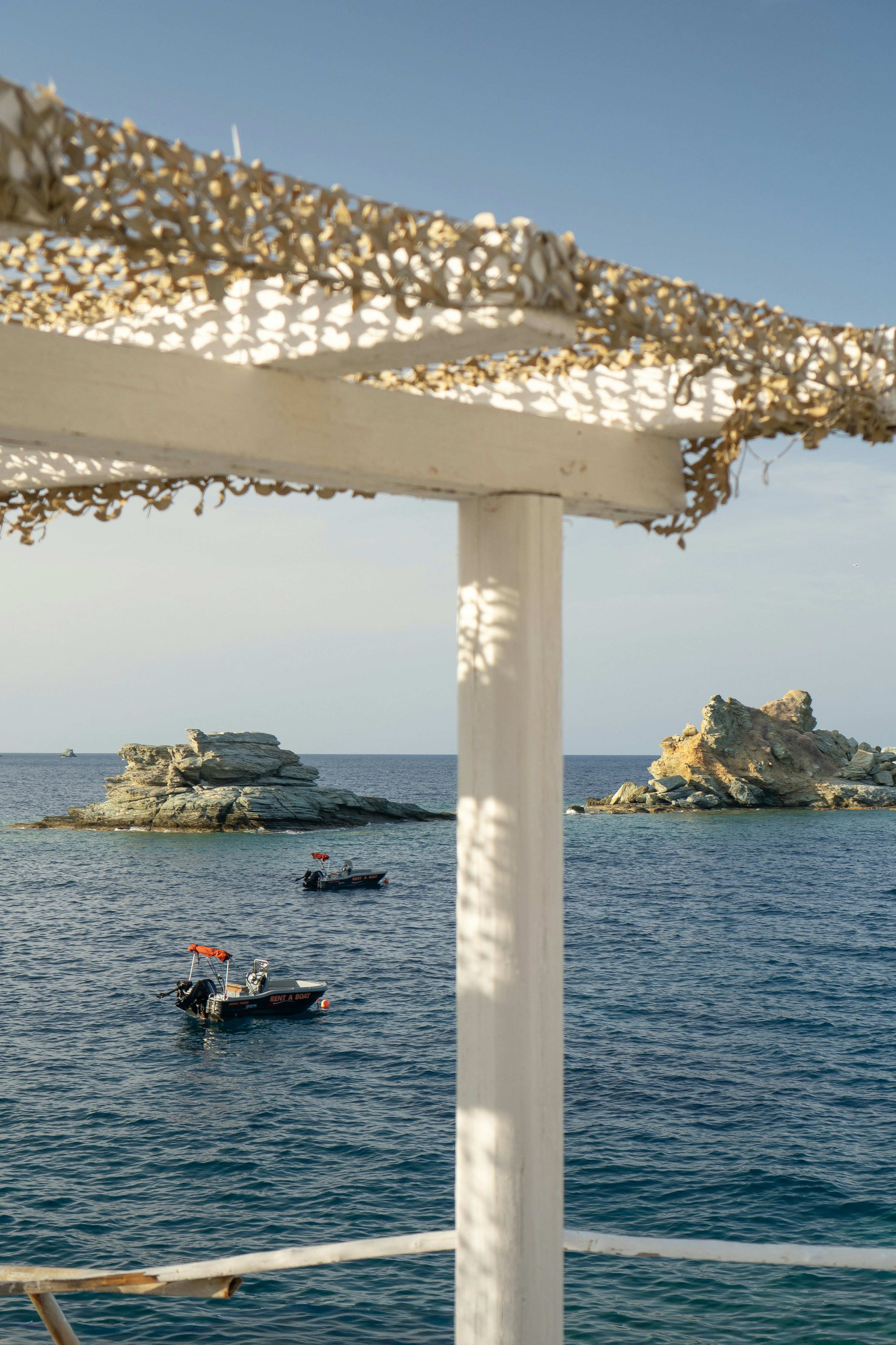 Fishing boats navigate calm waters framed by rocky outcrops under a clear sky. The scene captures a tranquil moment in a coastal setting.