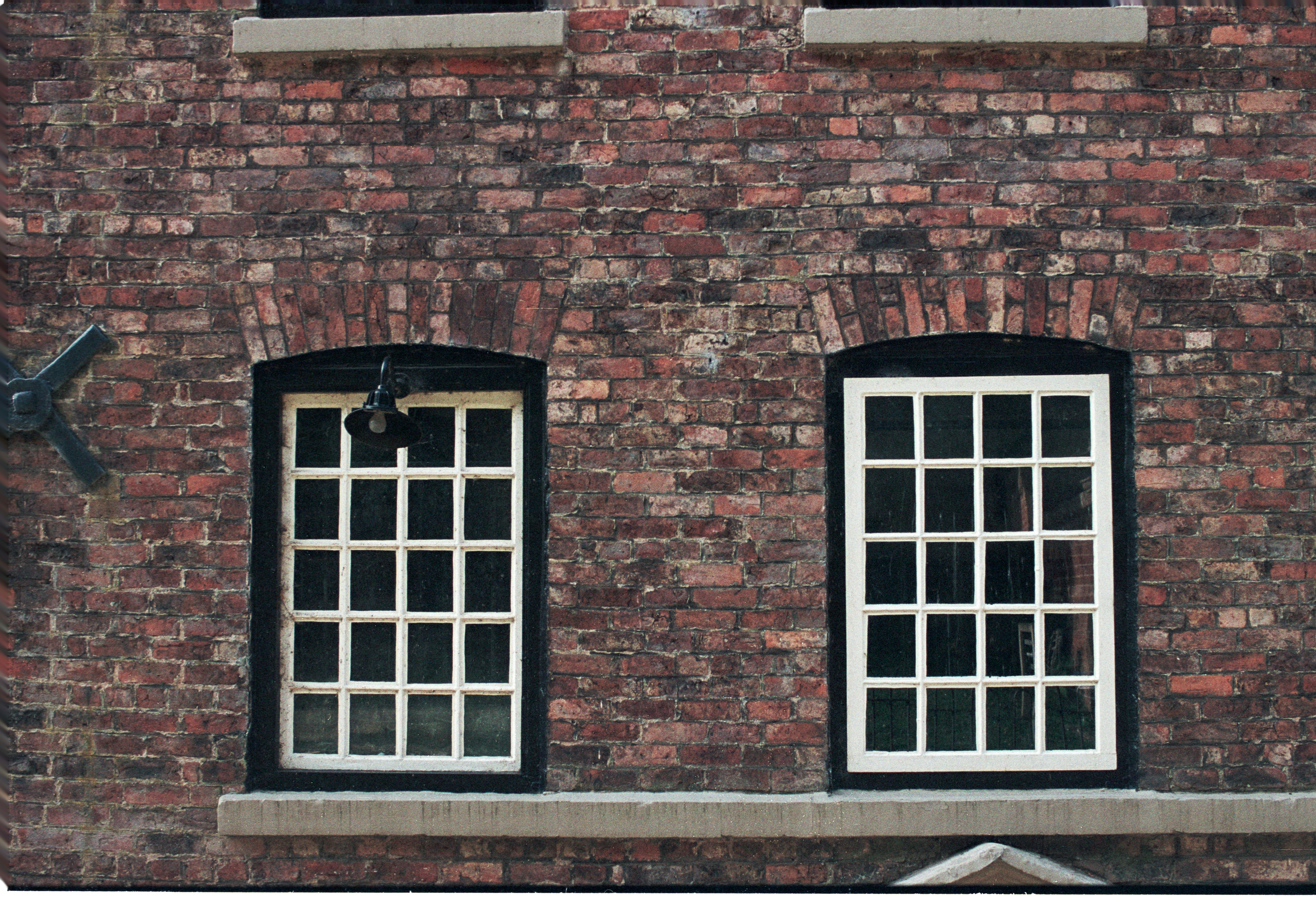Two symmetrical windows framed by a textured brick wall, showcasing classic architectural design elements.