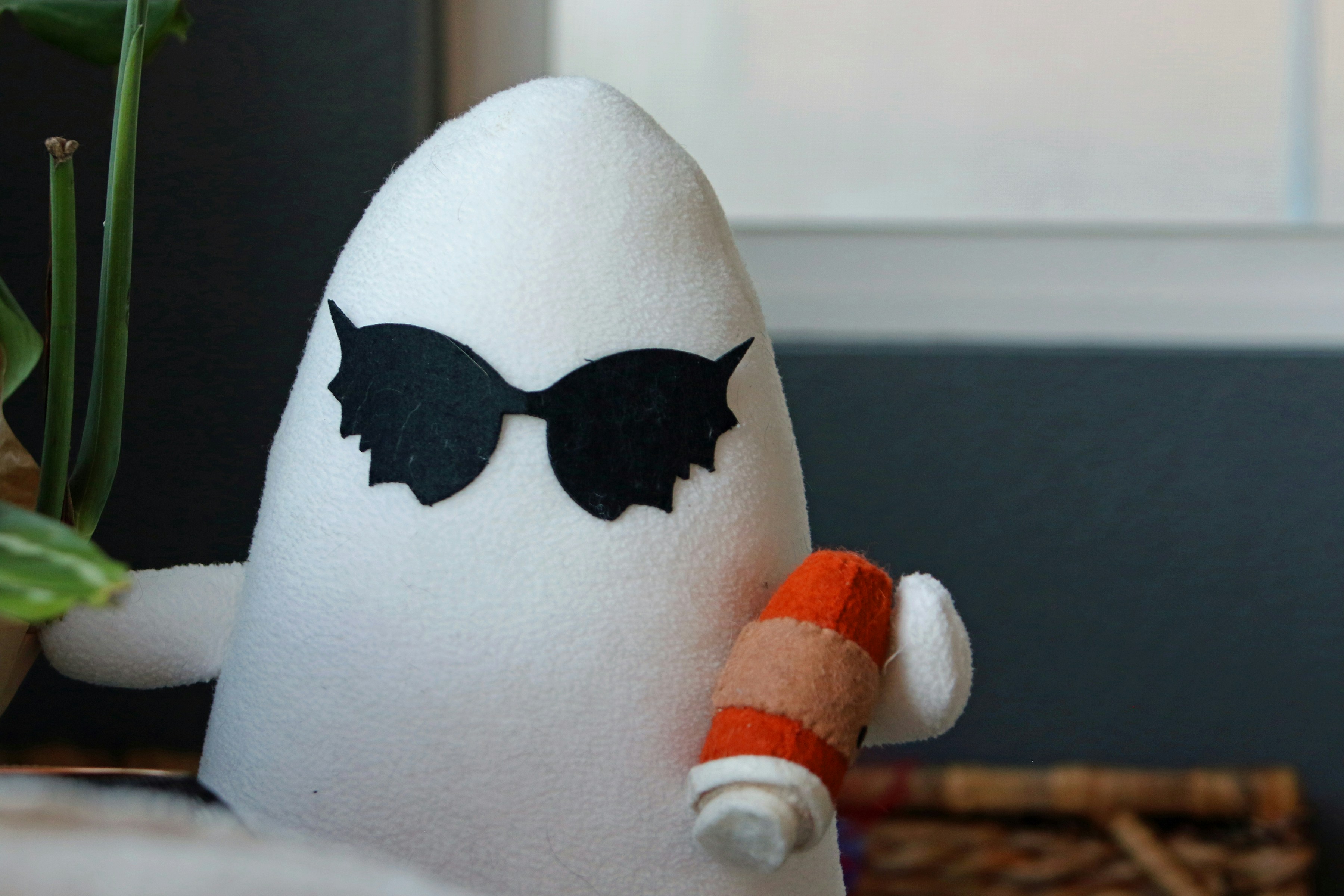 A plush ghost wearing sunglasses holds a candy cane.