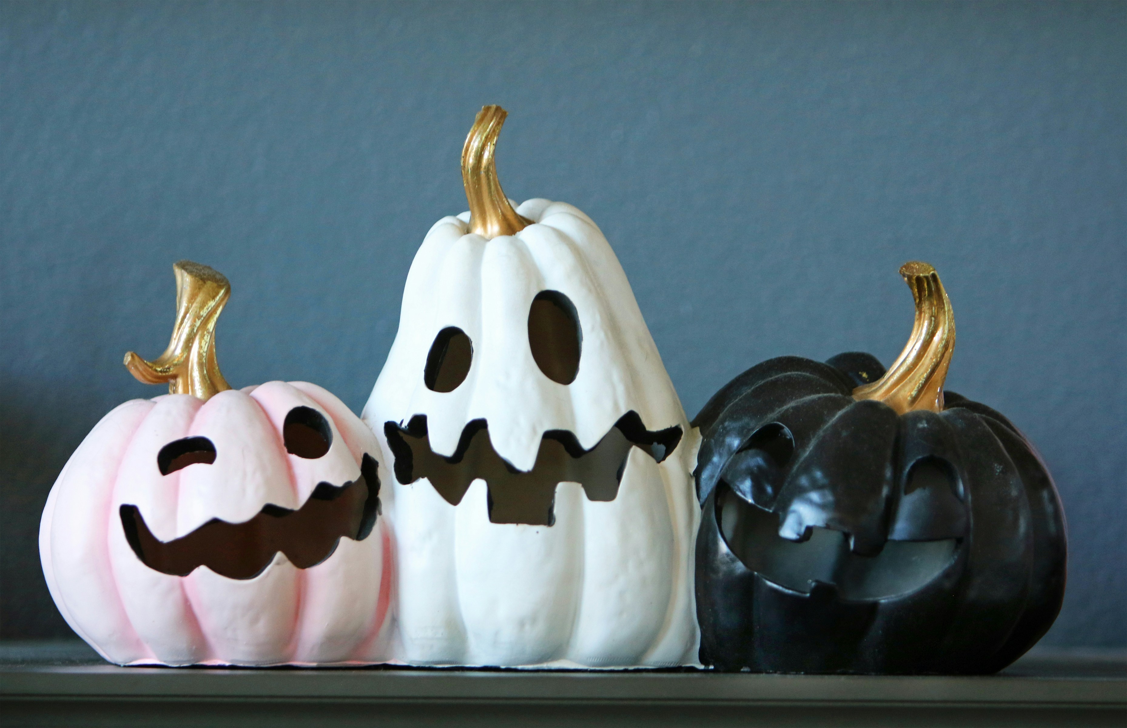  trio of carved pumpkins on a shelf under a blue wall