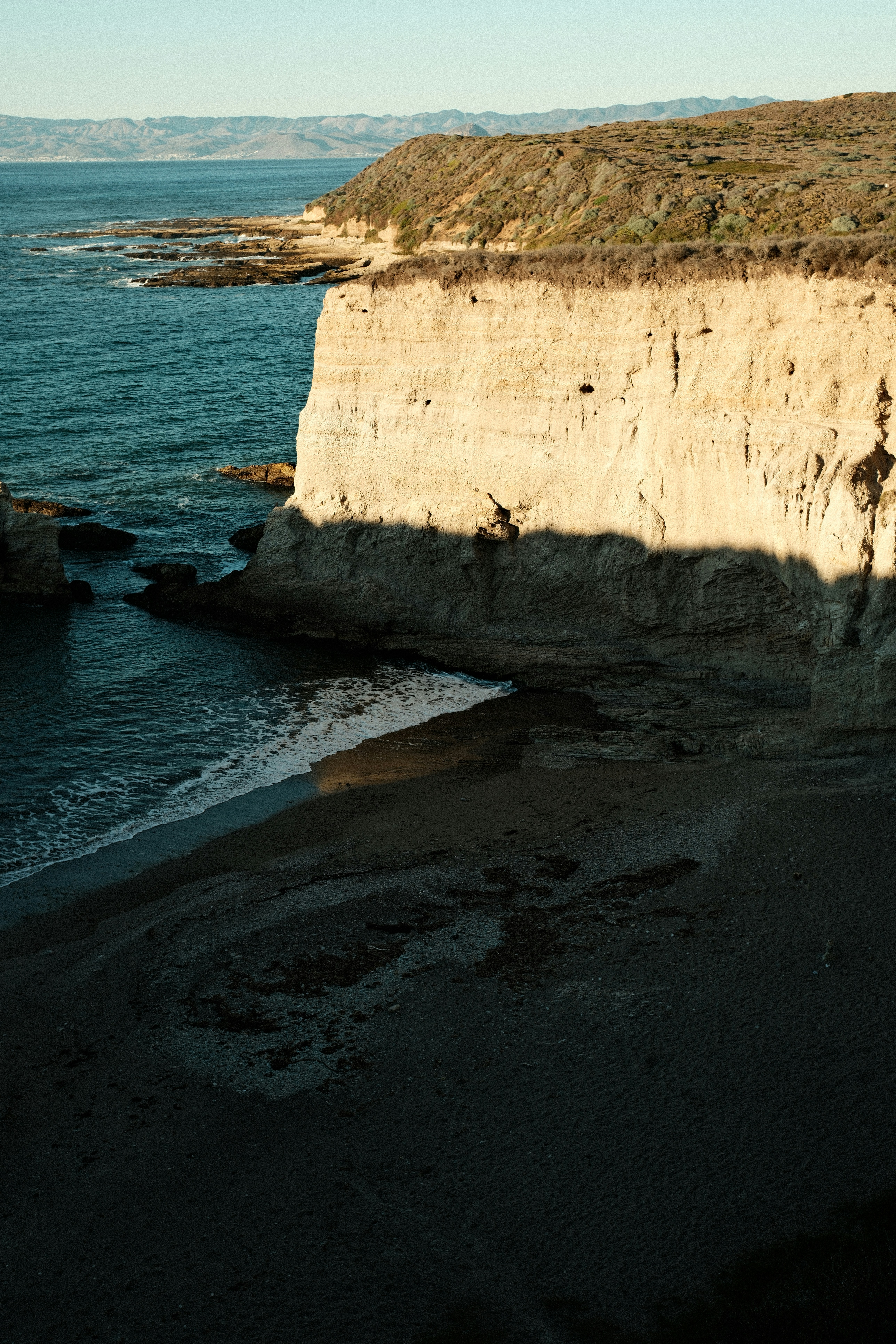 Rugged cliffside meeting the tranquil sea, highlighting the interplay of land and water. The shadows cast by the cliffs accentuate the natural textures of the landscape.