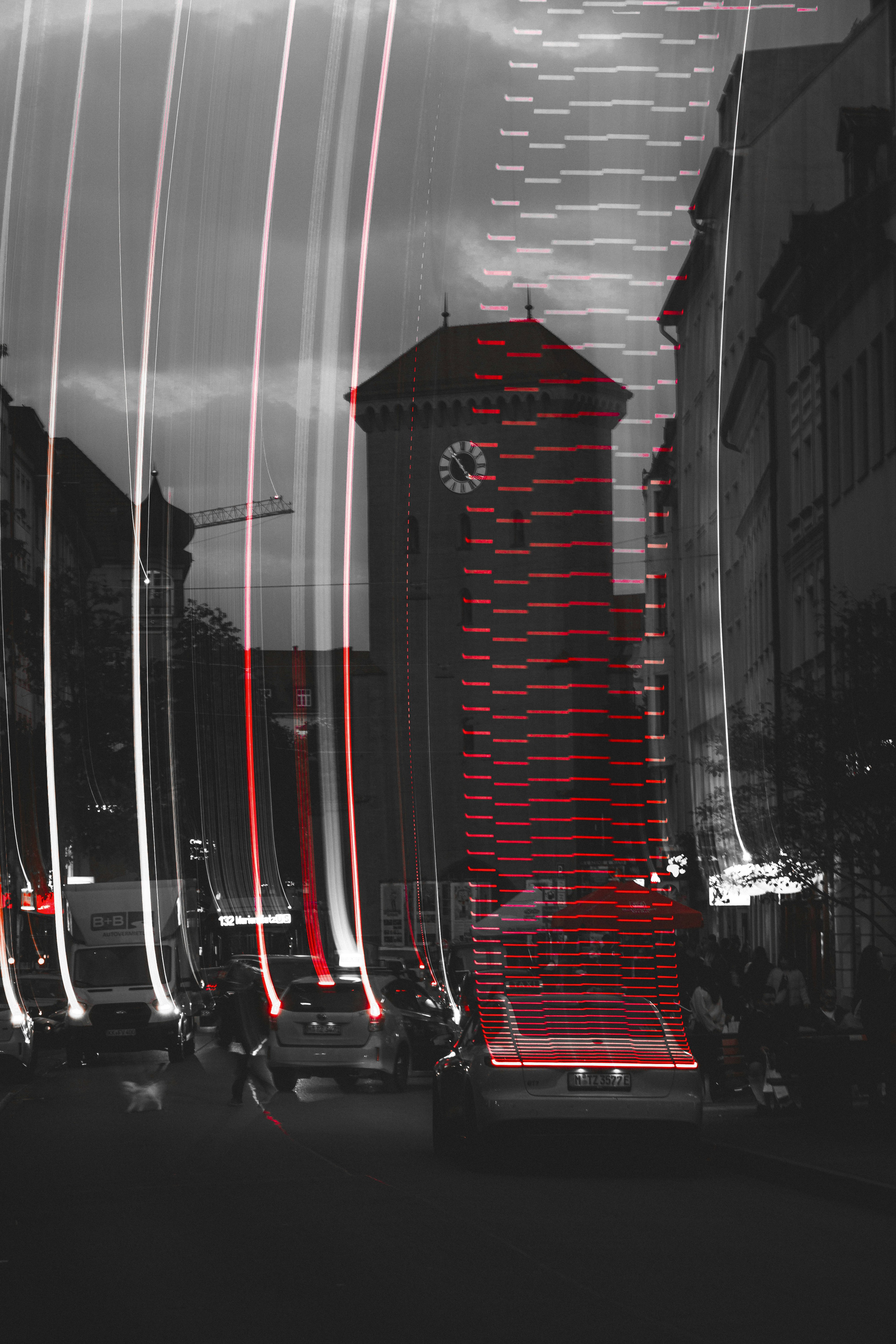 Long exposure shot capturing the dynamic flow of traffic with a historic clock tower in the backdrop. The scene is accentuated by streaks of red and white light against a monochromatic cityscape.