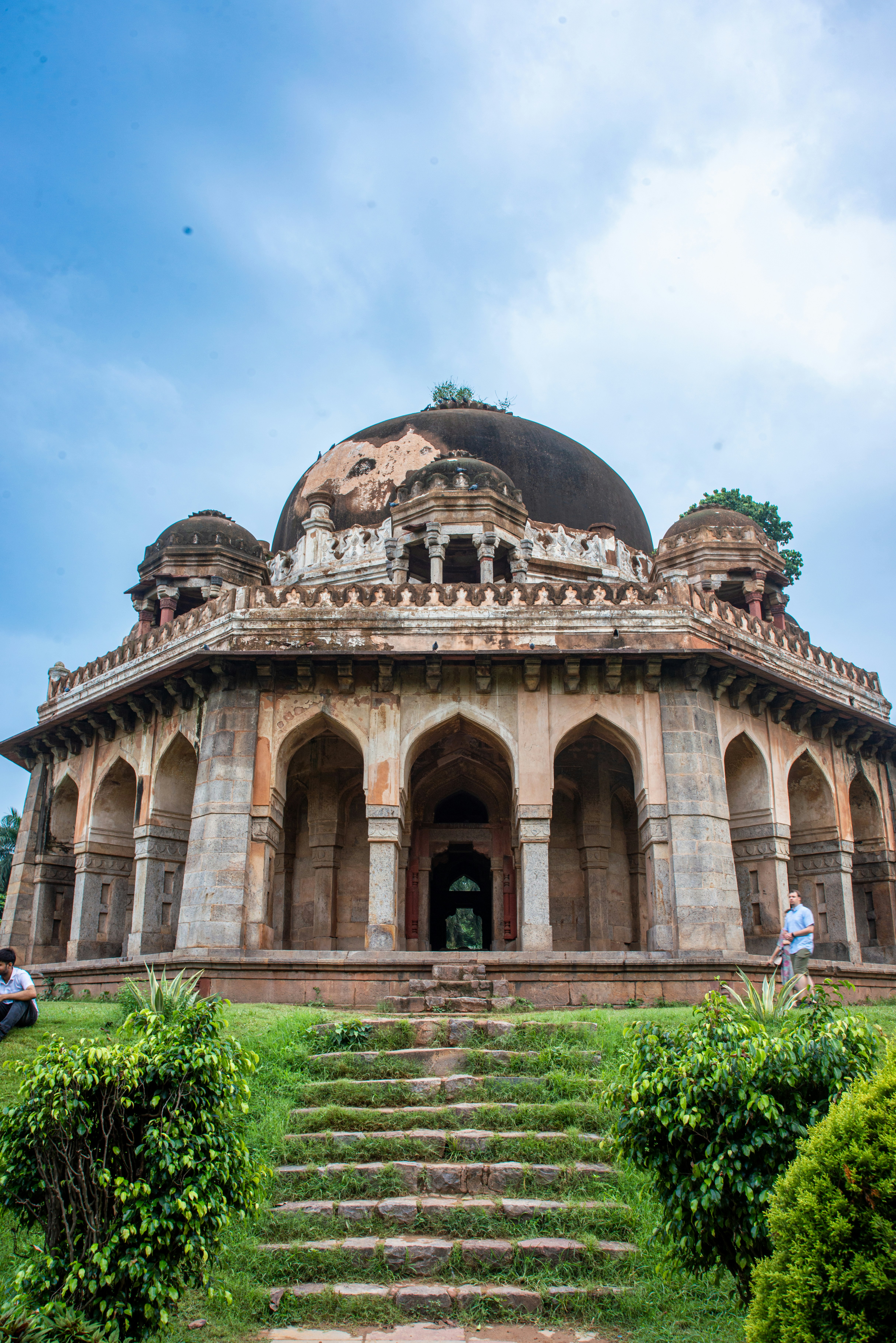 Historic dome structure surrounded by lush greenery and stone steps, showcasing intricate architectural details.