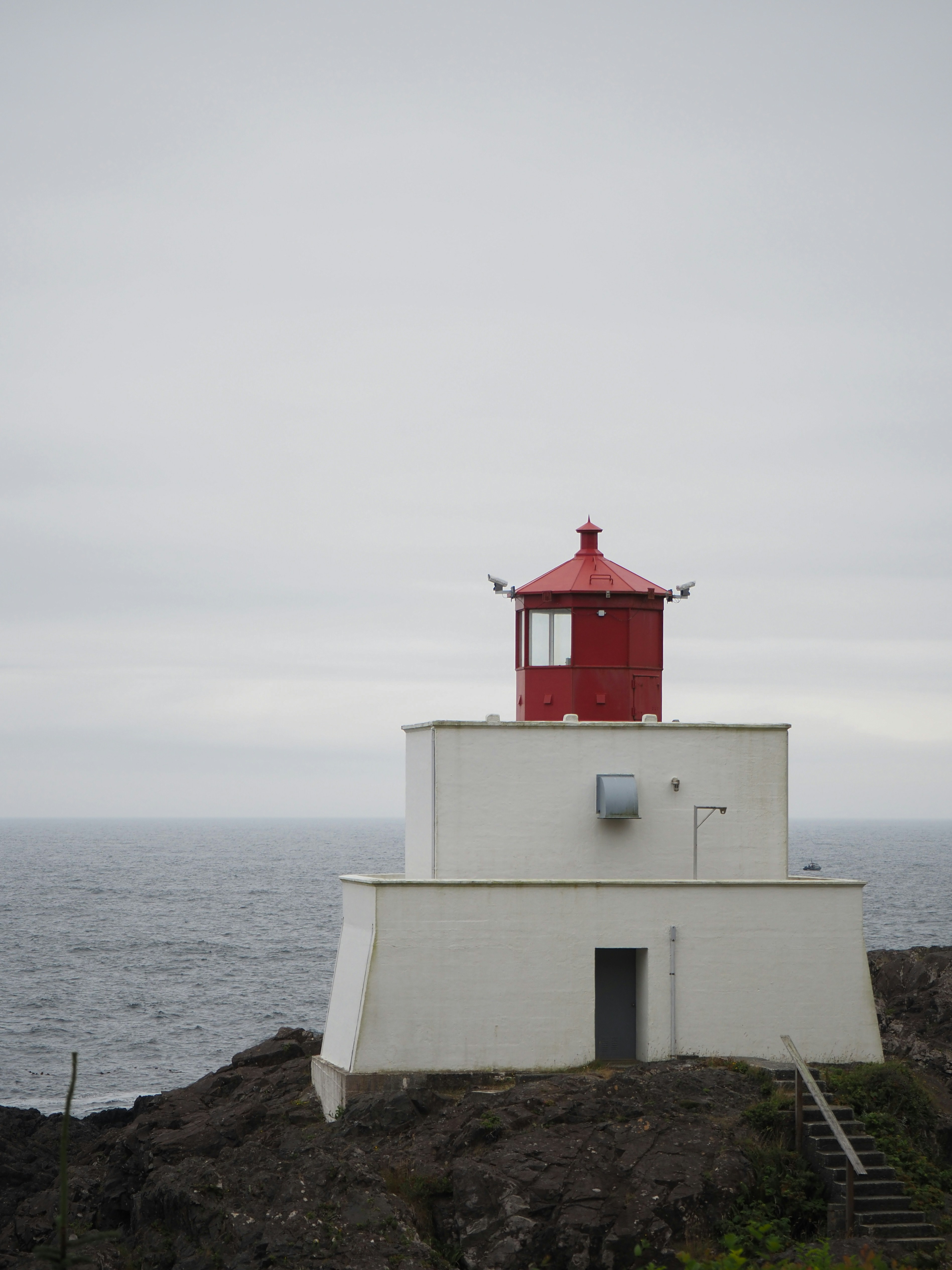 Red lighthouse perched on rocky coastline, overlooking the vast ocean under a cloudy sky.