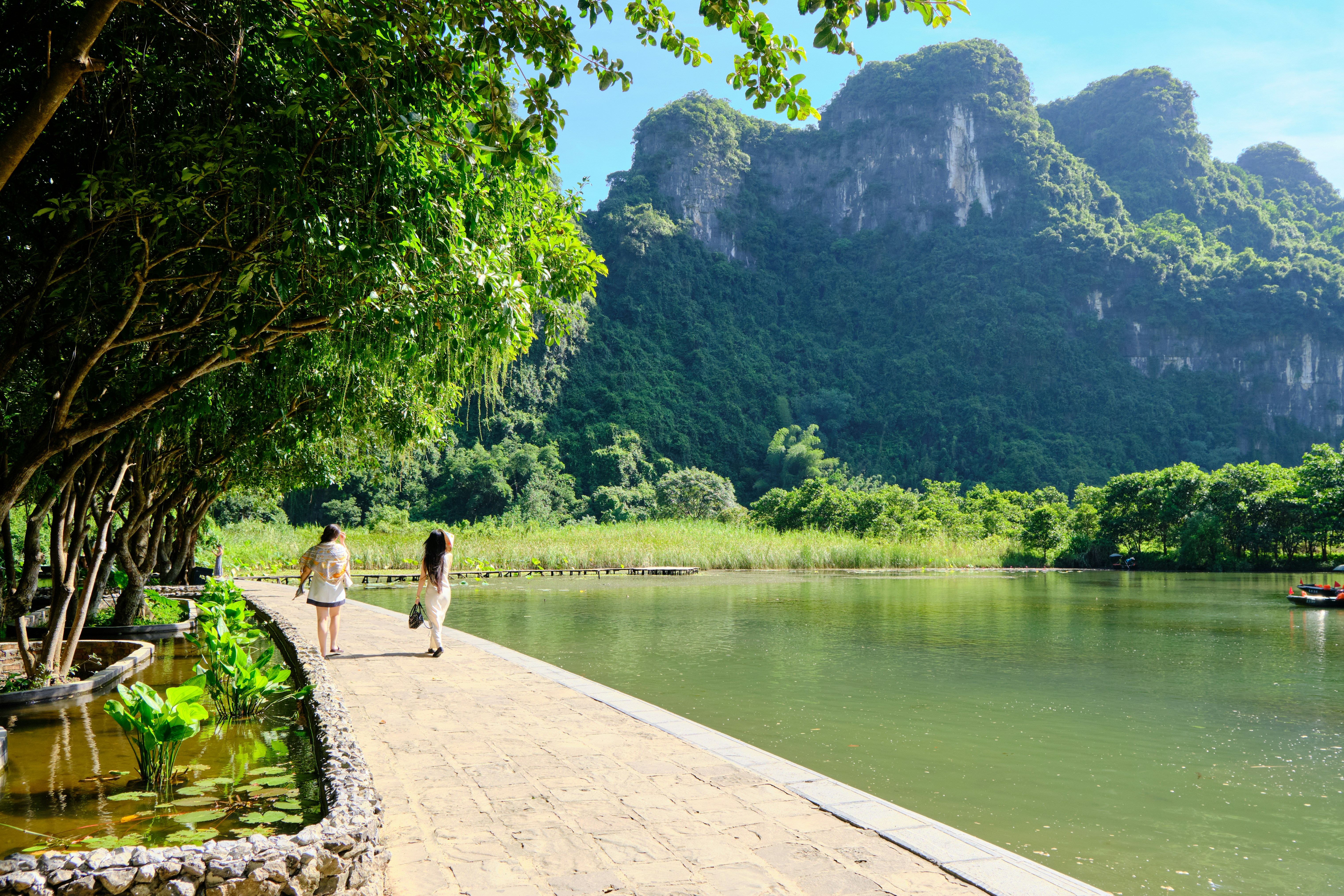 Two women walk along a path by a lake.