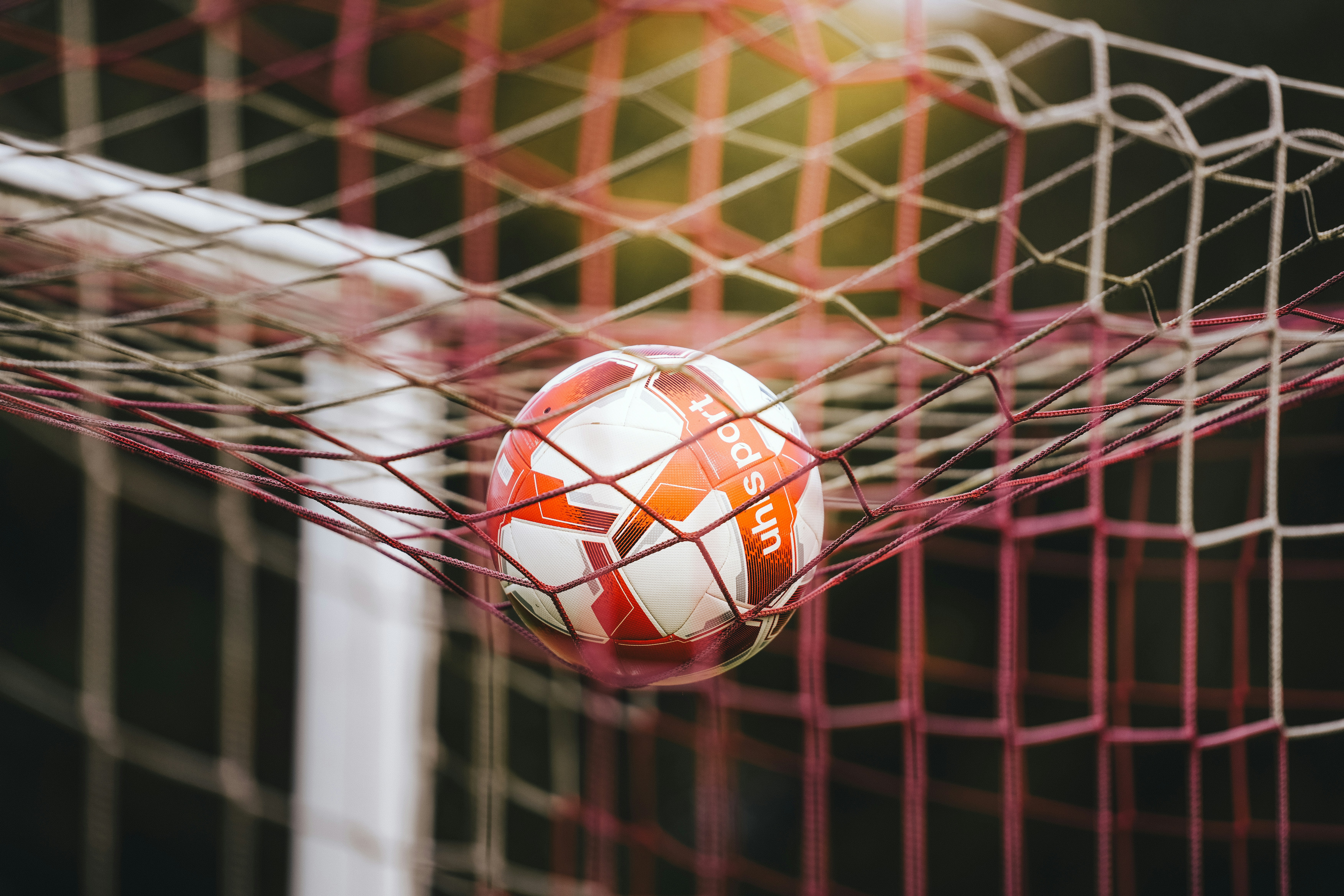 Soccer ball nestling in the net of a goal, captured mid-action during a match. The intricate details of the netting and ball emphasize the excitement of the game.